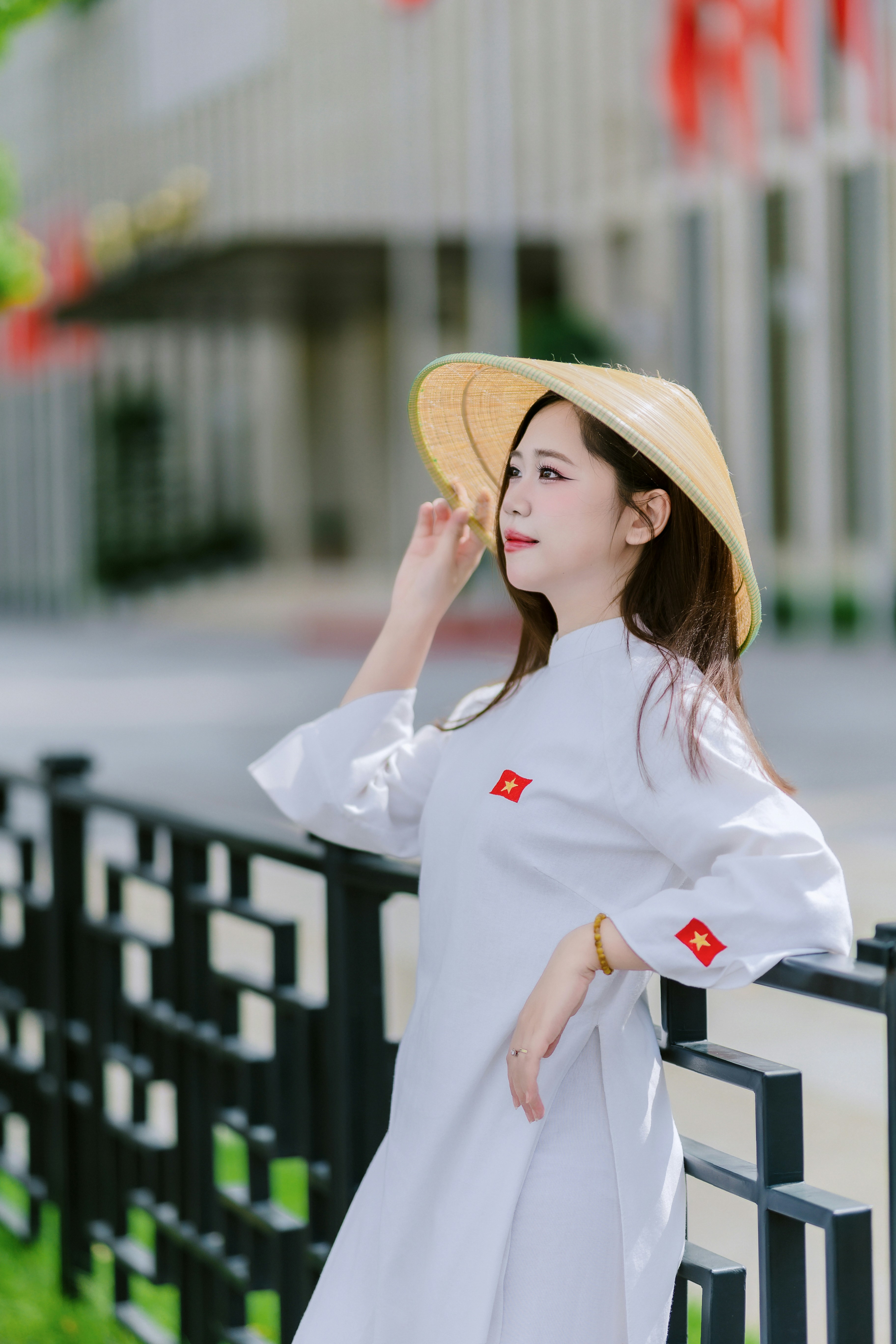 Woman in traditional attire with a conical hat, gracefully posed against a contemporary urban backdrop.