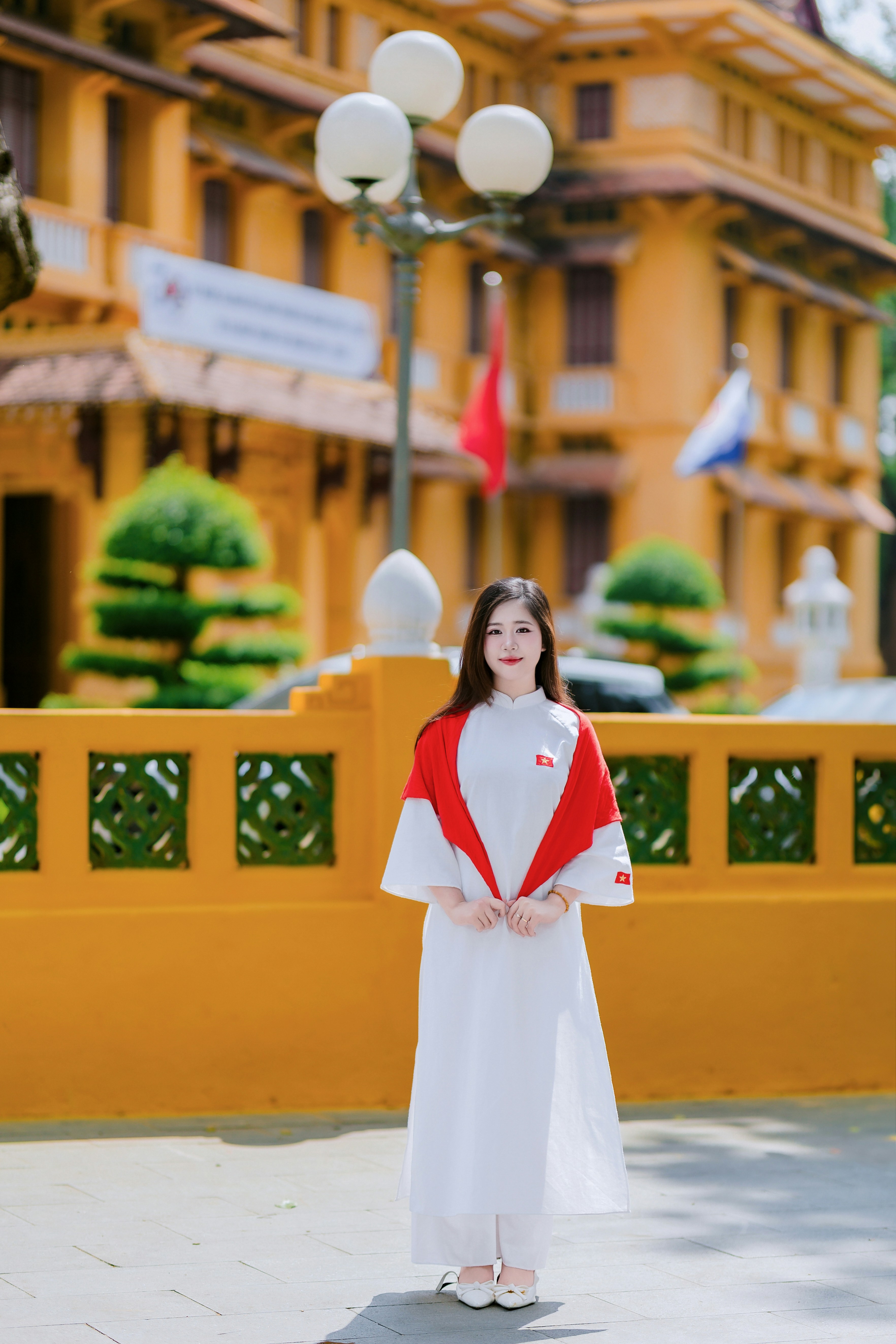 Vietnamese girl in ao dai celebrates national day | A young woman in a white dress stands outside a building.