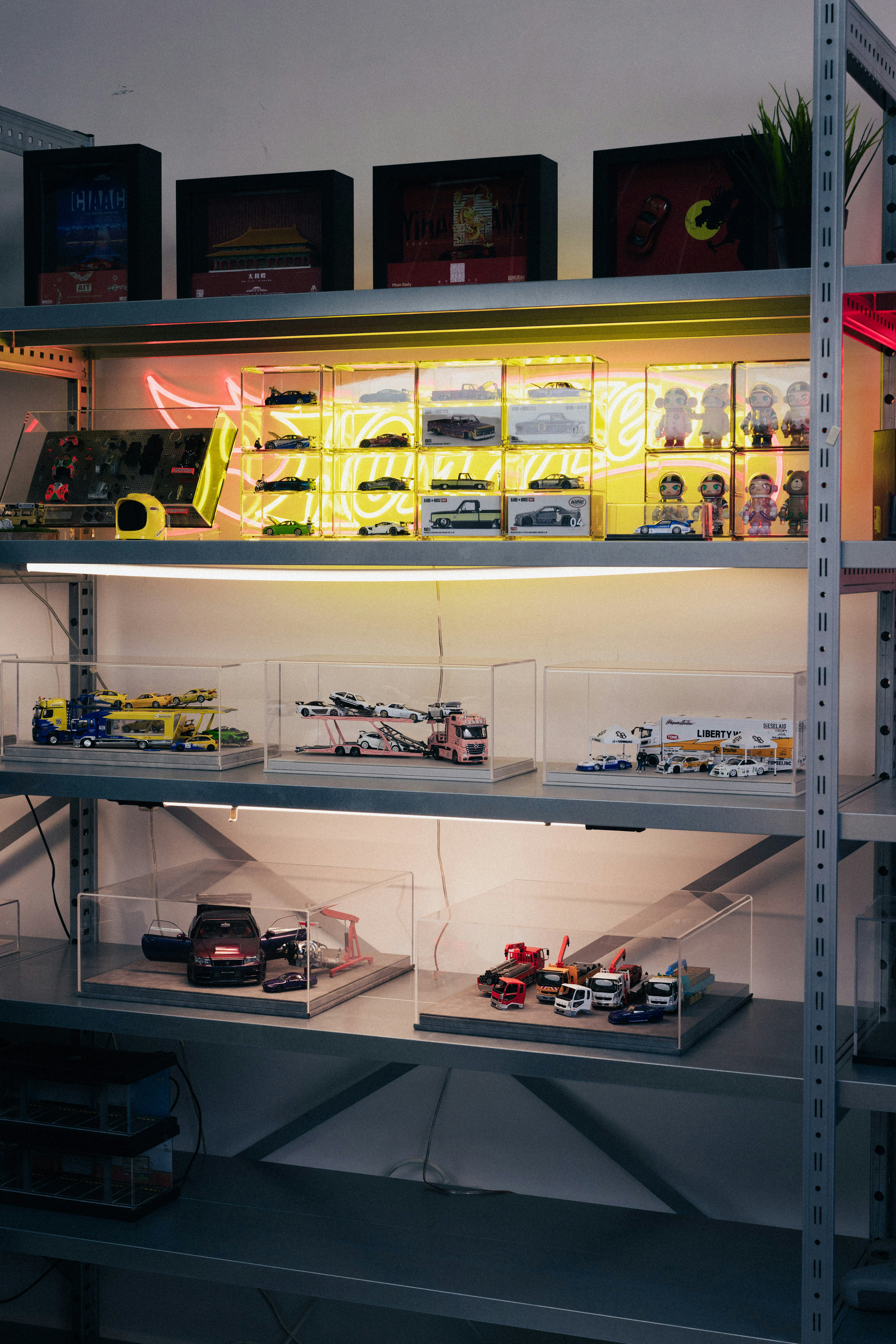 Colorful collection of miniature vehicles and figurines arranged on shelves, illuminated by a neon sign. The display showcases a blend of nostalgia and craftsmanship.