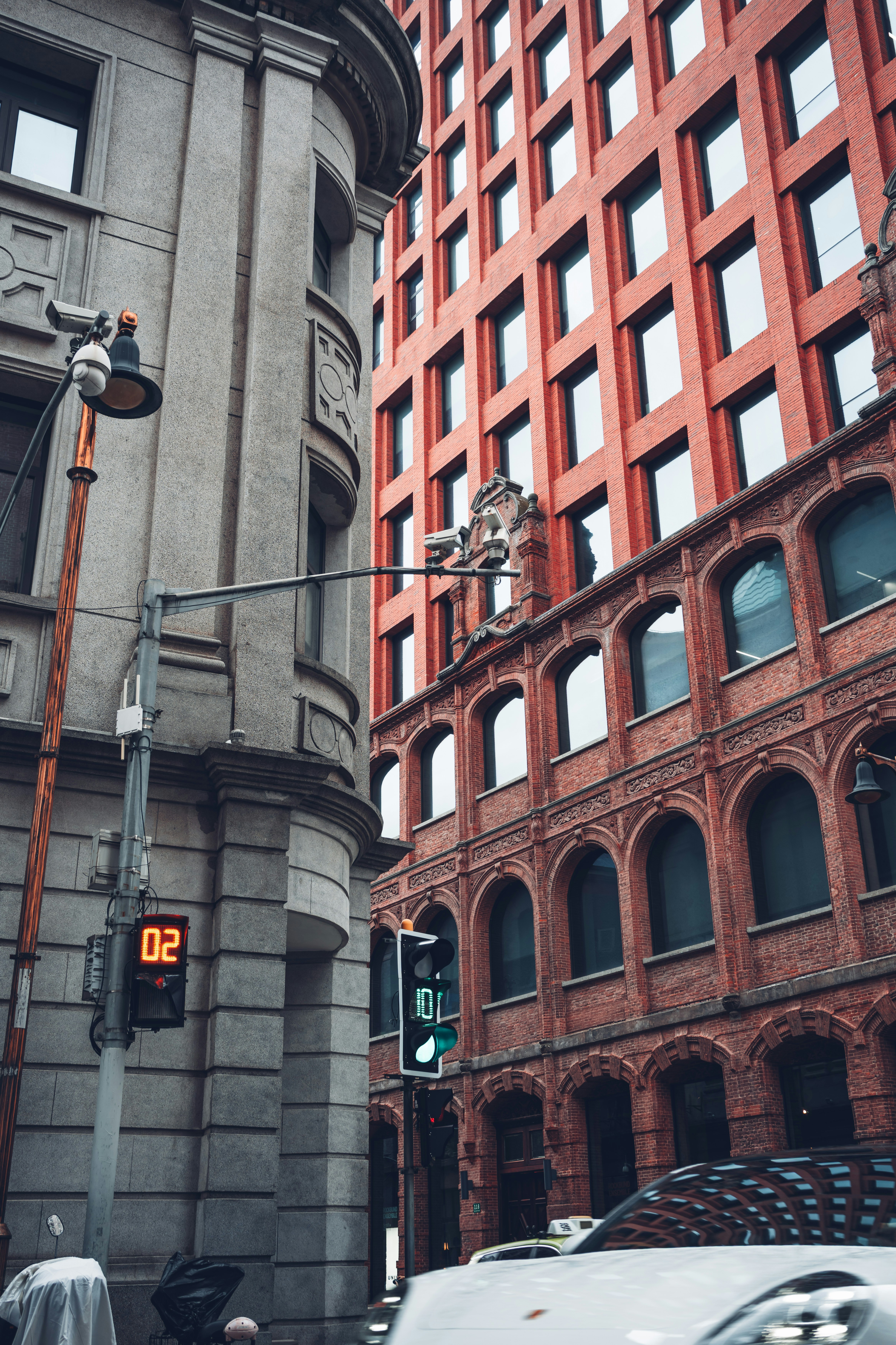 Architectural juxtaposition of a classic stone building and a modern red-brick facade, with traffic signals and vehicles adding urban life.