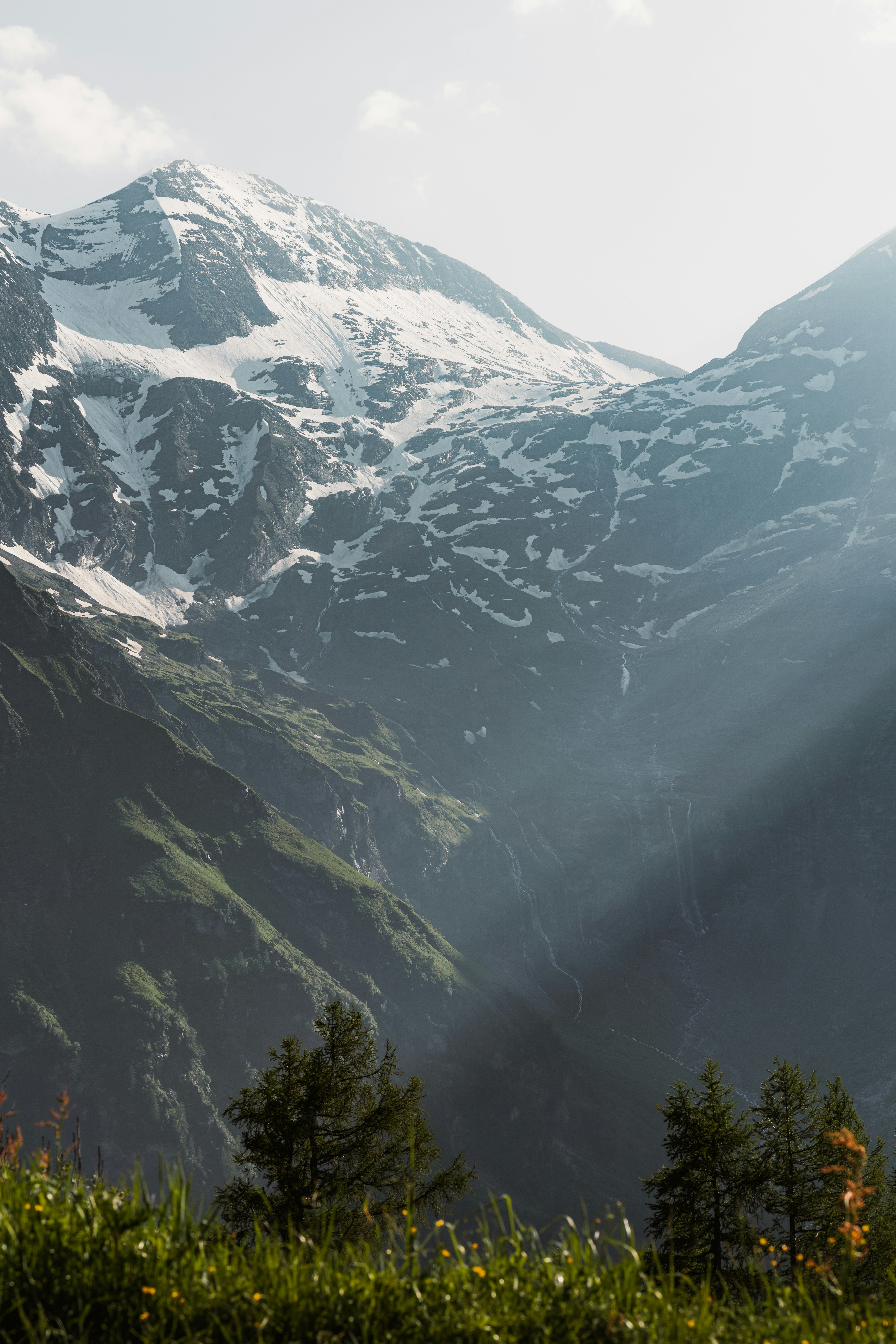 Alpine Peaks Illuminated by Morning Sunrays | Snow-capped mountains rise above a green valley