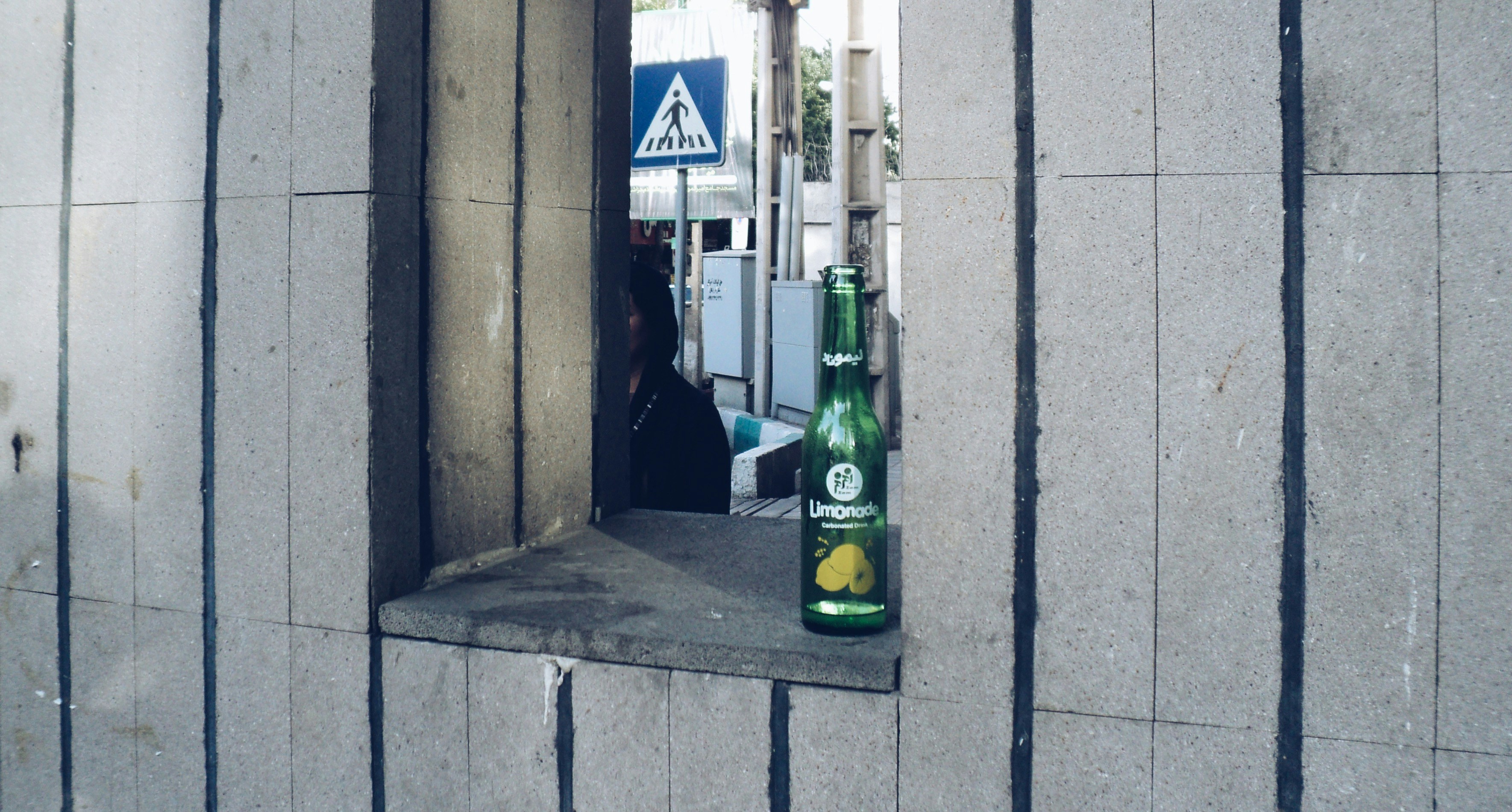 A little bit of green in a world of grey. | Green bottle on a concrete ledge with street background