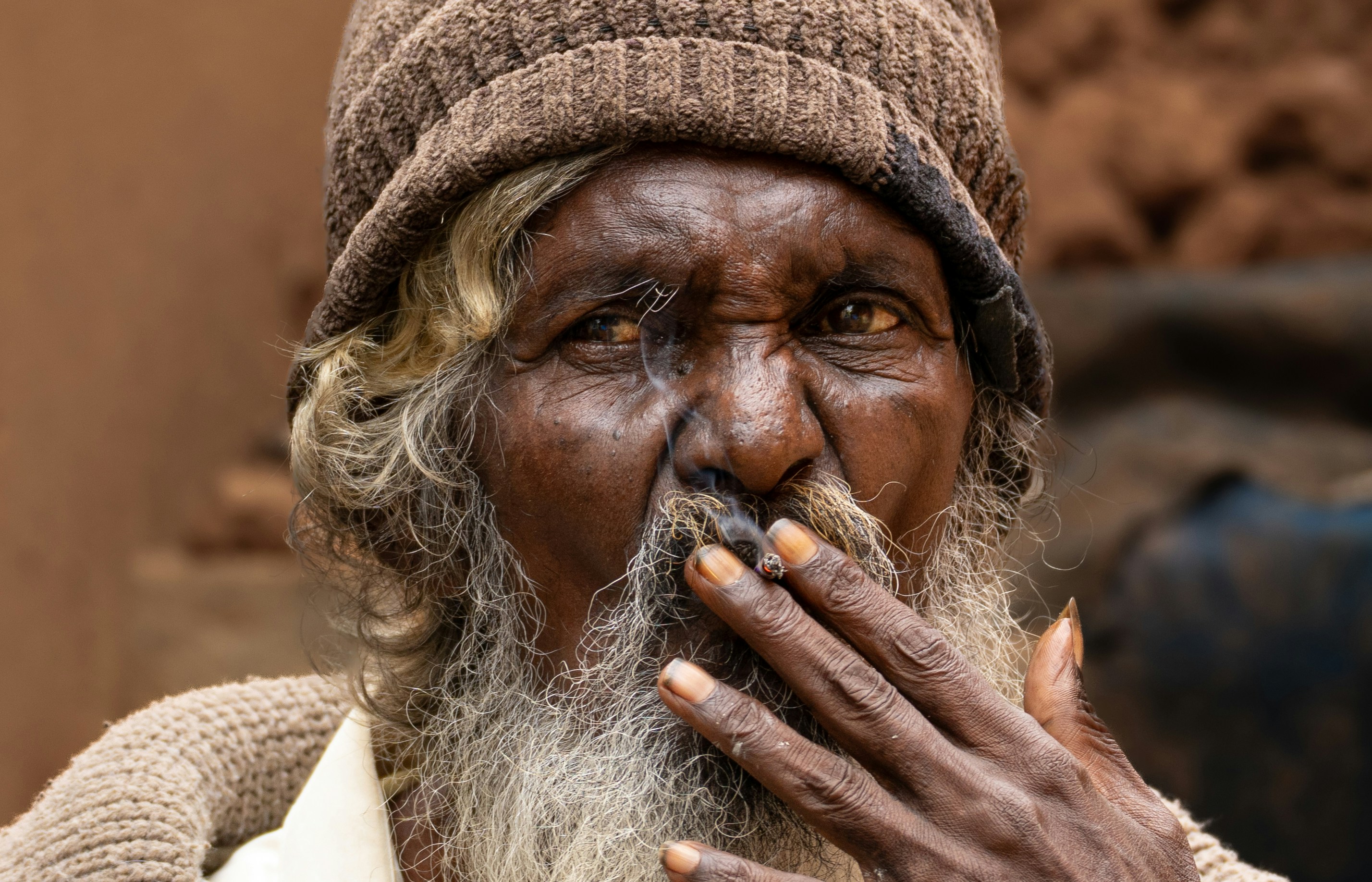 Elderly Man with Wisdom: Close-Up Portrait of a Thoughtful Senior in Traditional Attire | Cultural Heritage Photography #Elderly #PortraitPhotography #CulturalHeritage #SeniorWisdom | Elderly man with a beard smoking a cigarette.