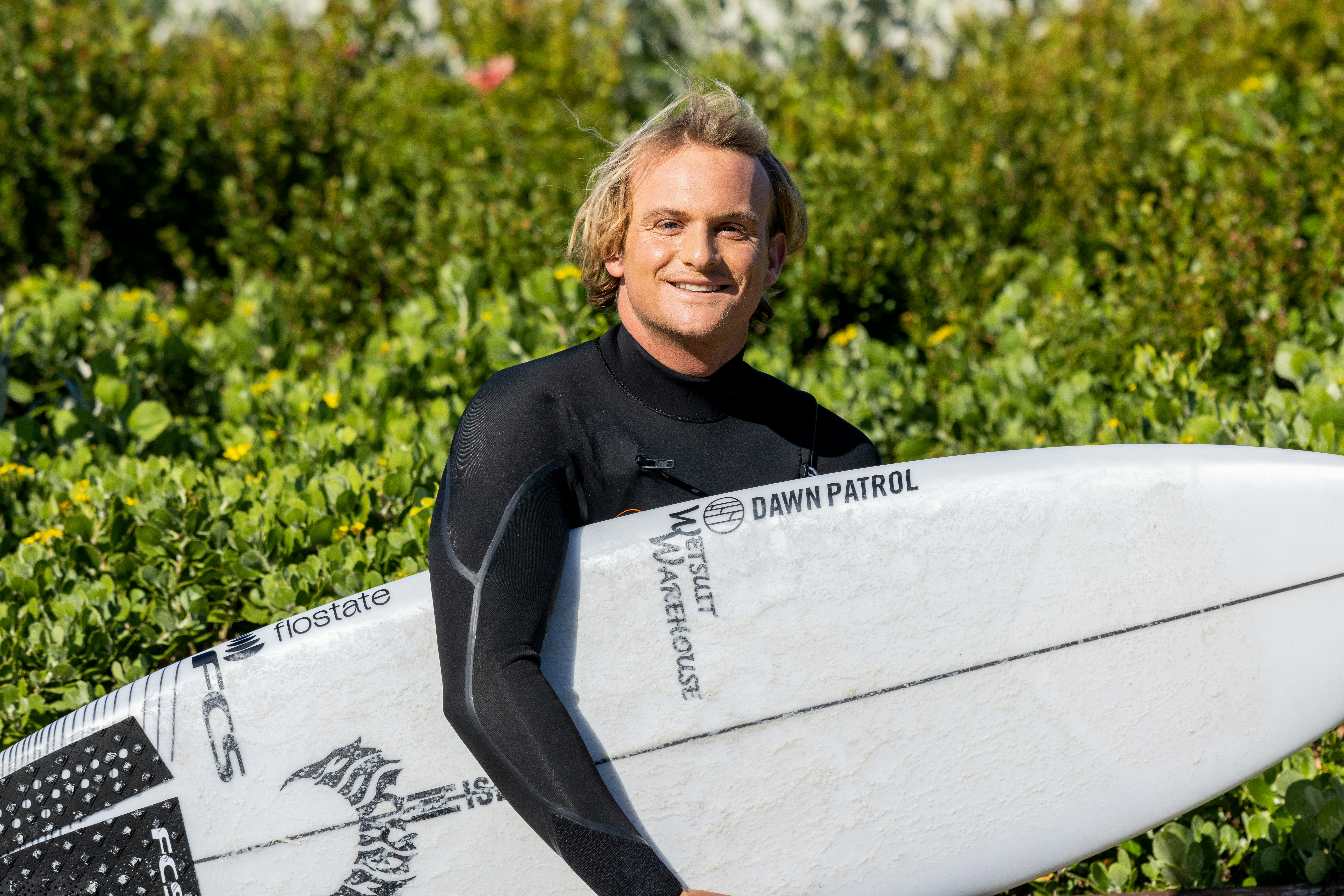 Surfer holding a surfboard with green foliage background