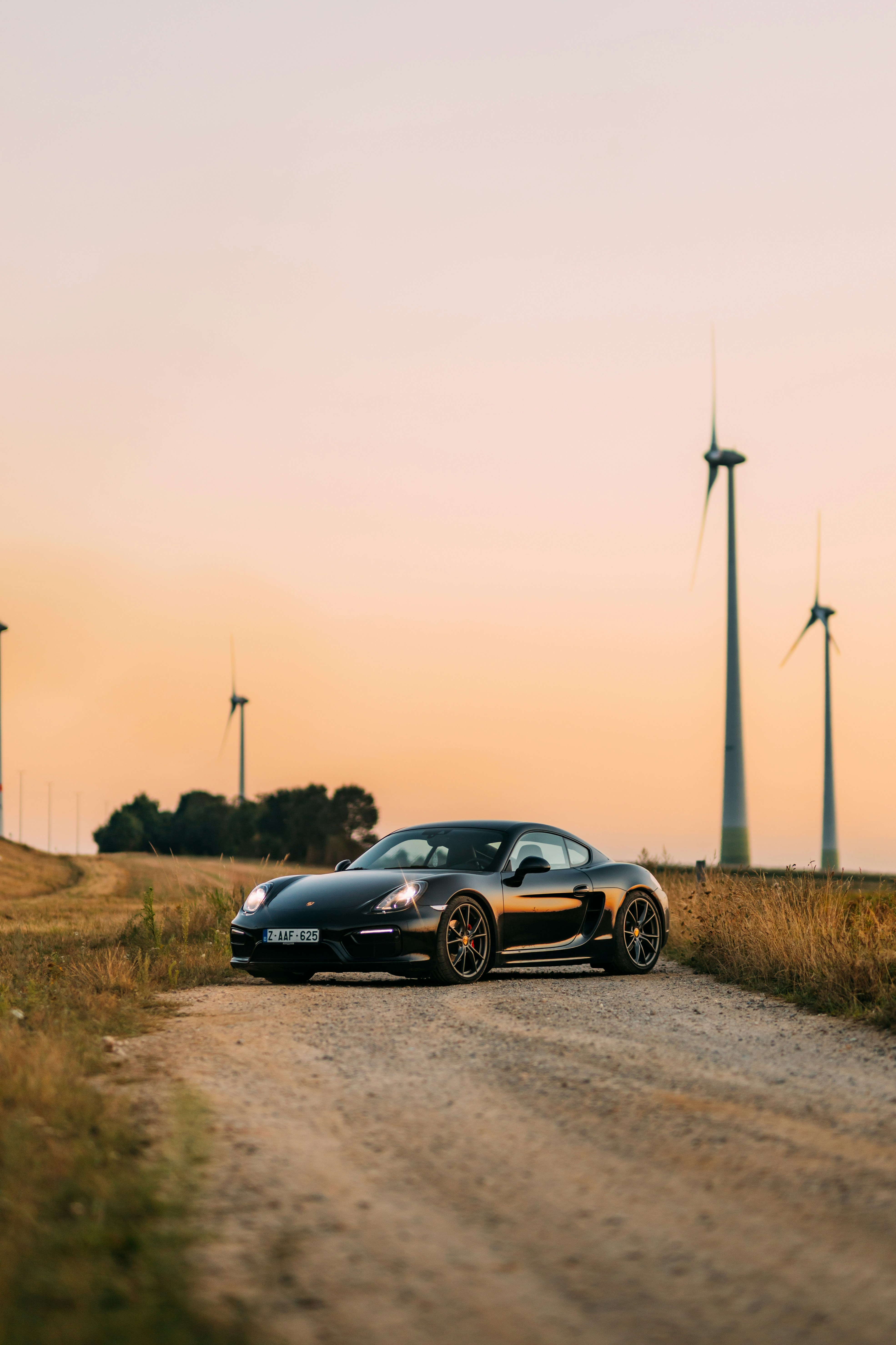 Black porsche on a dirt road with wind turbines