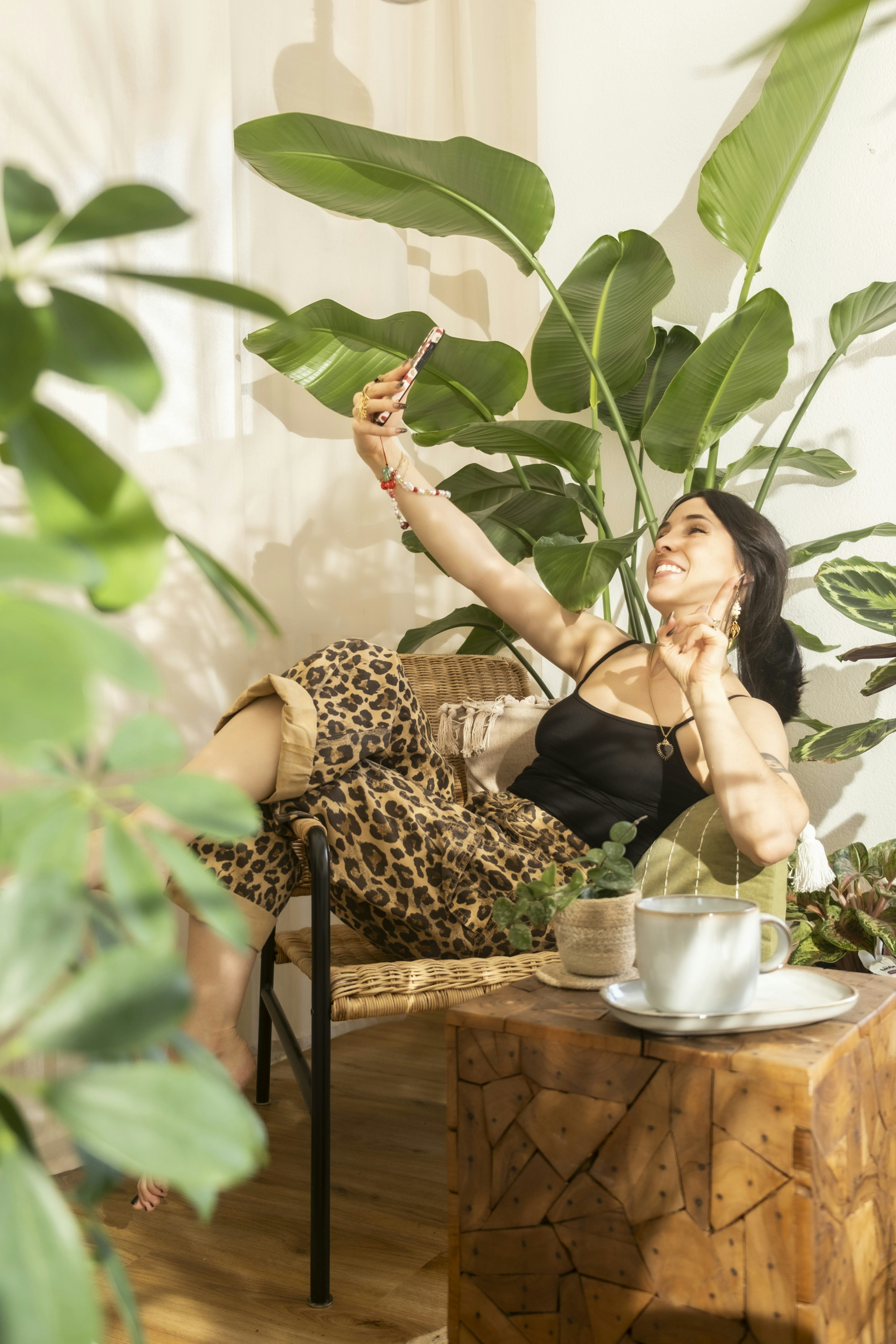 Woman taking a selfie while lounging in a cozy space surrounded by vibrant greenery. Sunlight filters through the leaves, creating a warm atmosphere.