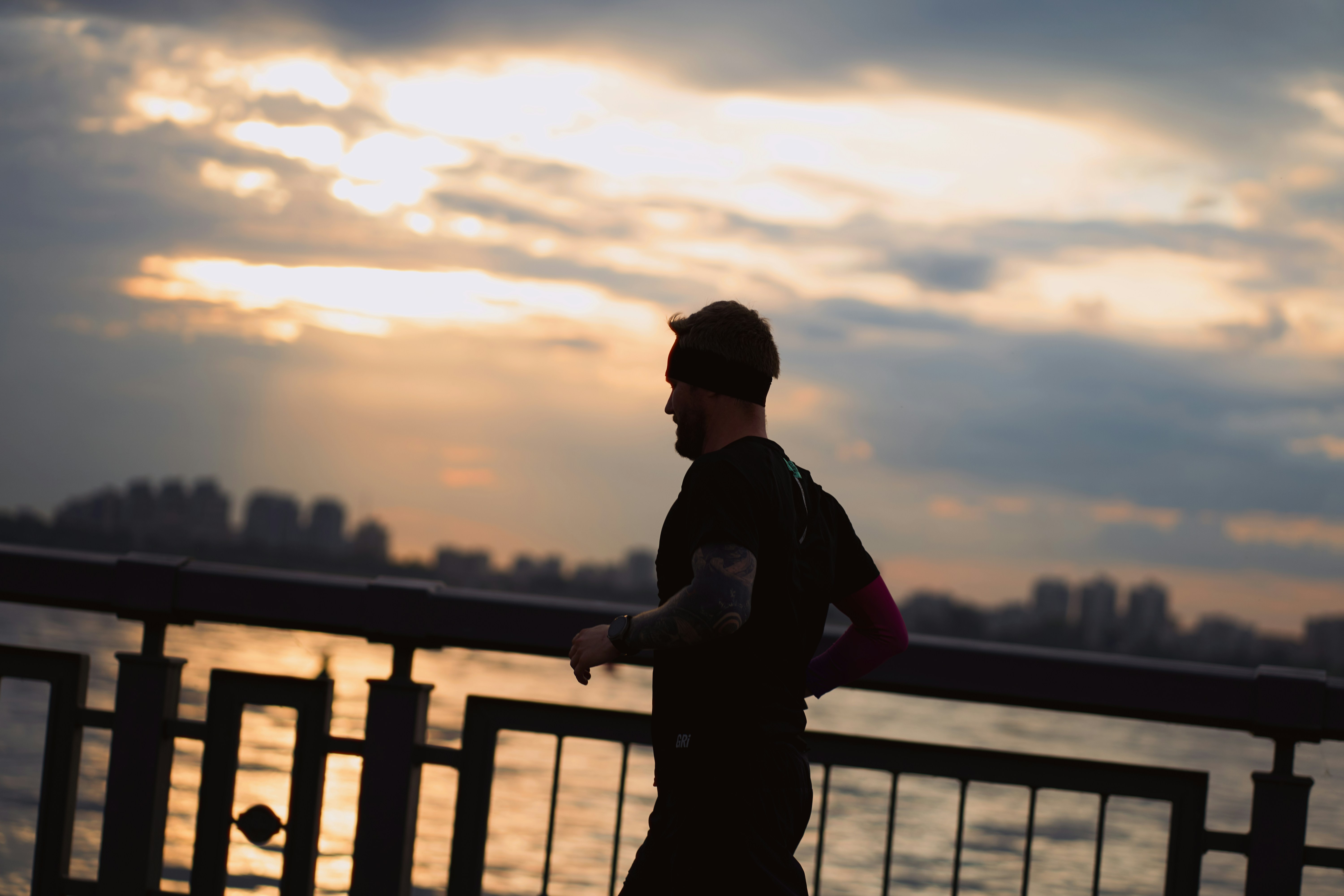 A runner silhouetted against a vibrant sunset, gliding along a waterfront promenade. The scene captures the essence of evening exercise and tranquility.