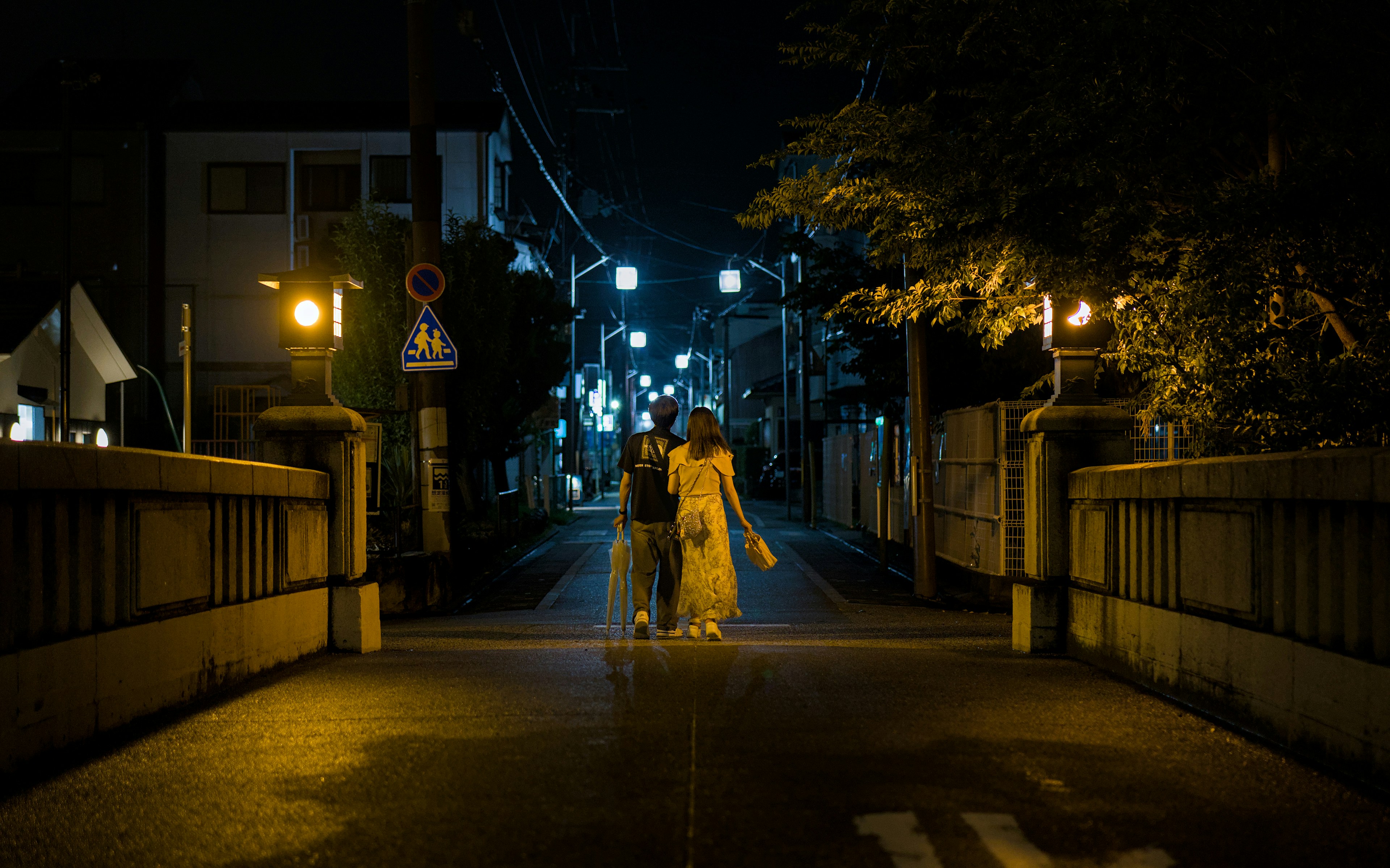 A couple is walking over the Horai Bridge (蓬莱橋) near Chushojima Station (中書島駅) in Kyoto, Japan. 2025-08-11 @ WQH5+XX7 | A person walking through a dimly lit street at night