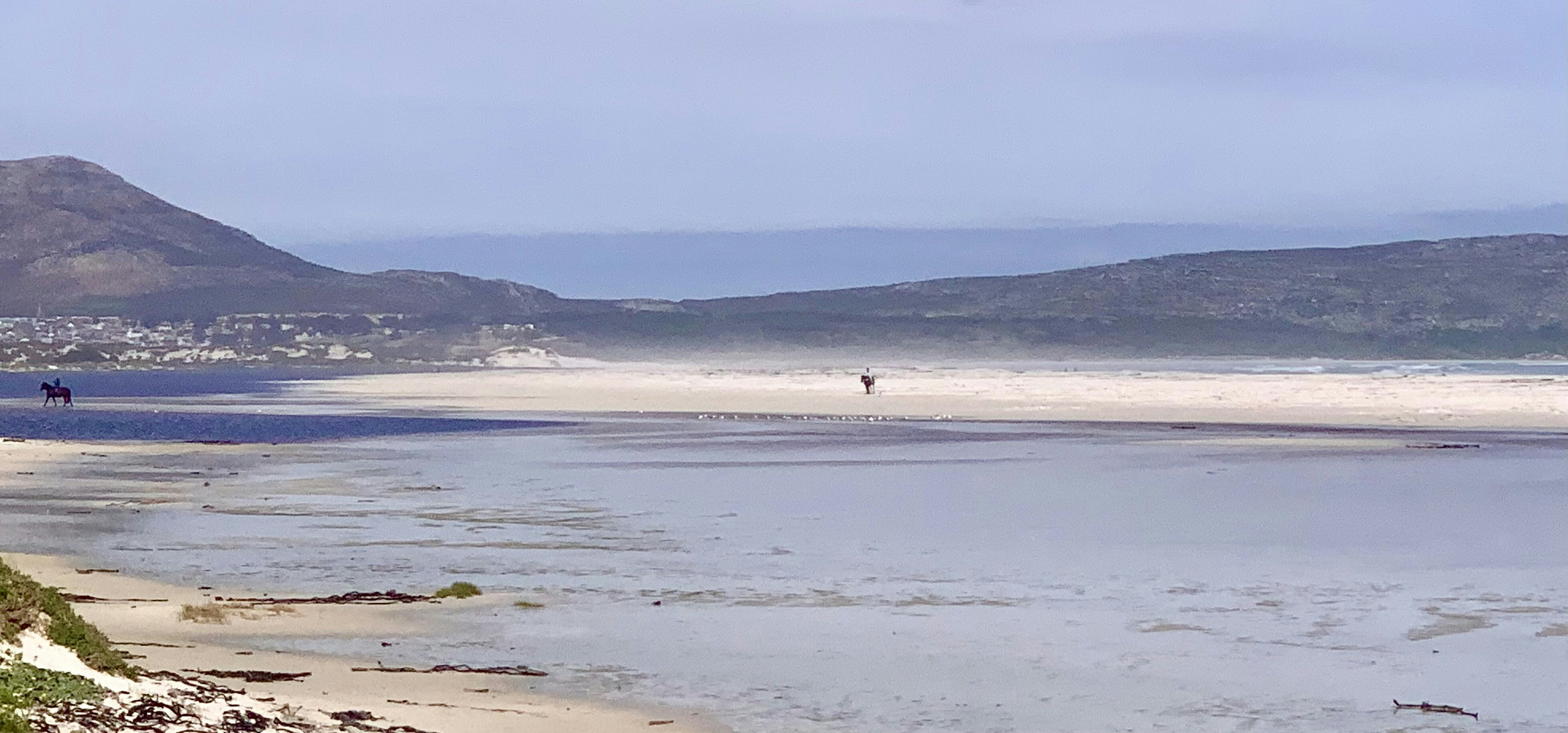 Gentle waves lapping against the sandy beach with a distant figure enjoying the tranquil atmosphere. A picturesque coastal landscape invites calm reflection.