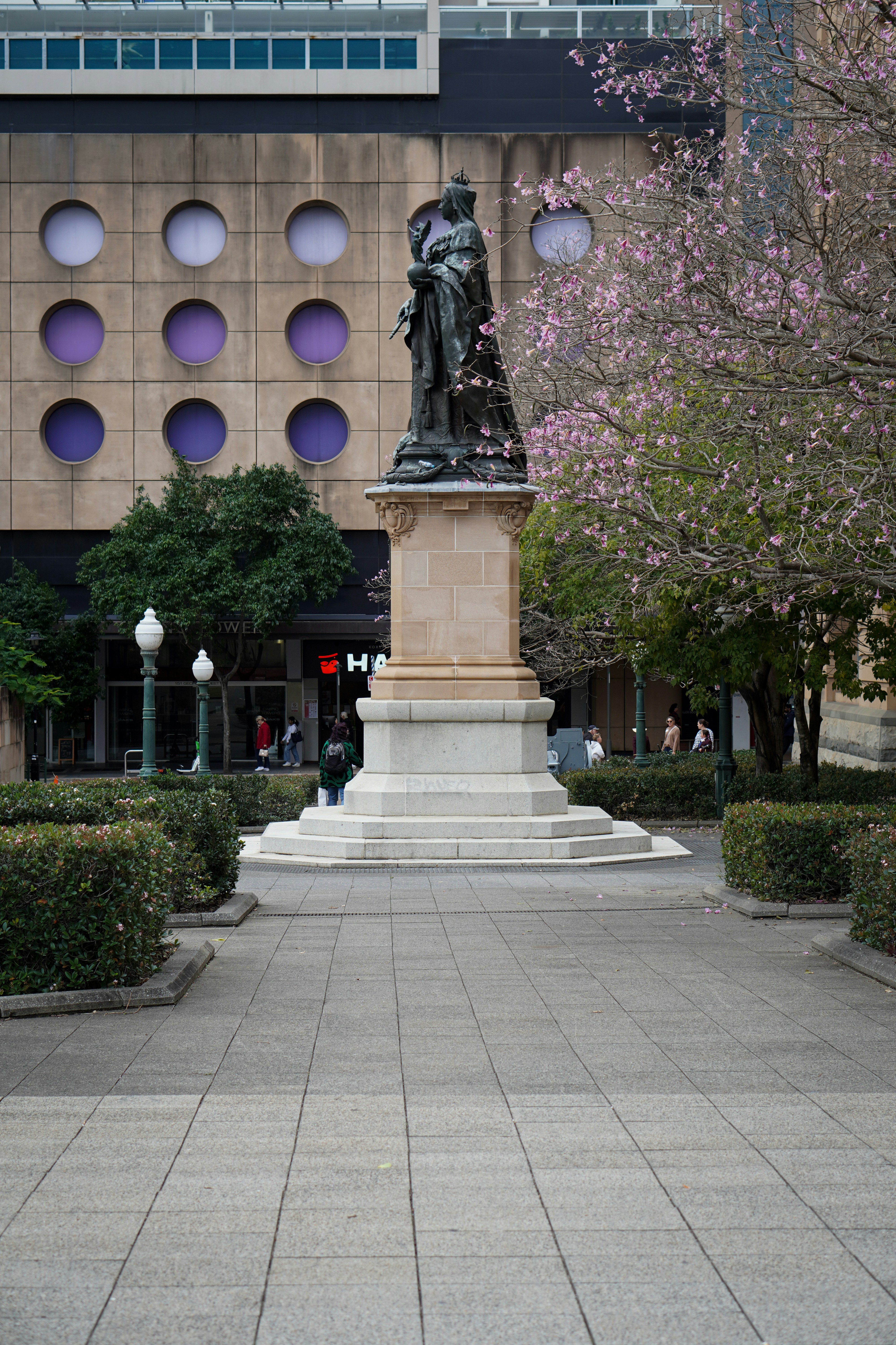 Queen Victoria Monument, George Street, Brisbane. | Statue in a park with cherry blossoms and modern building.