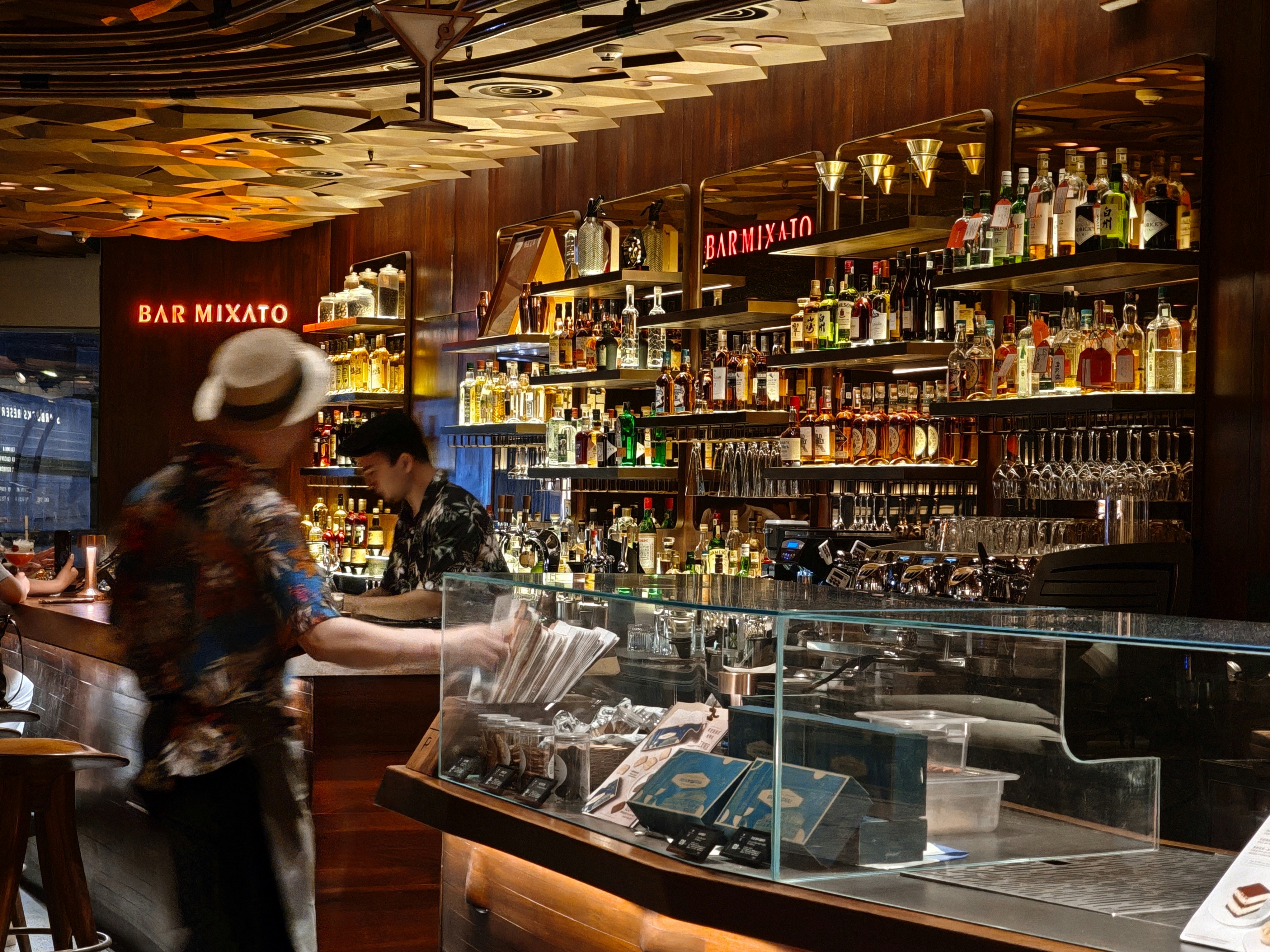 BAR MIXATO | Bartender serving drinks at a well-stocked bar.