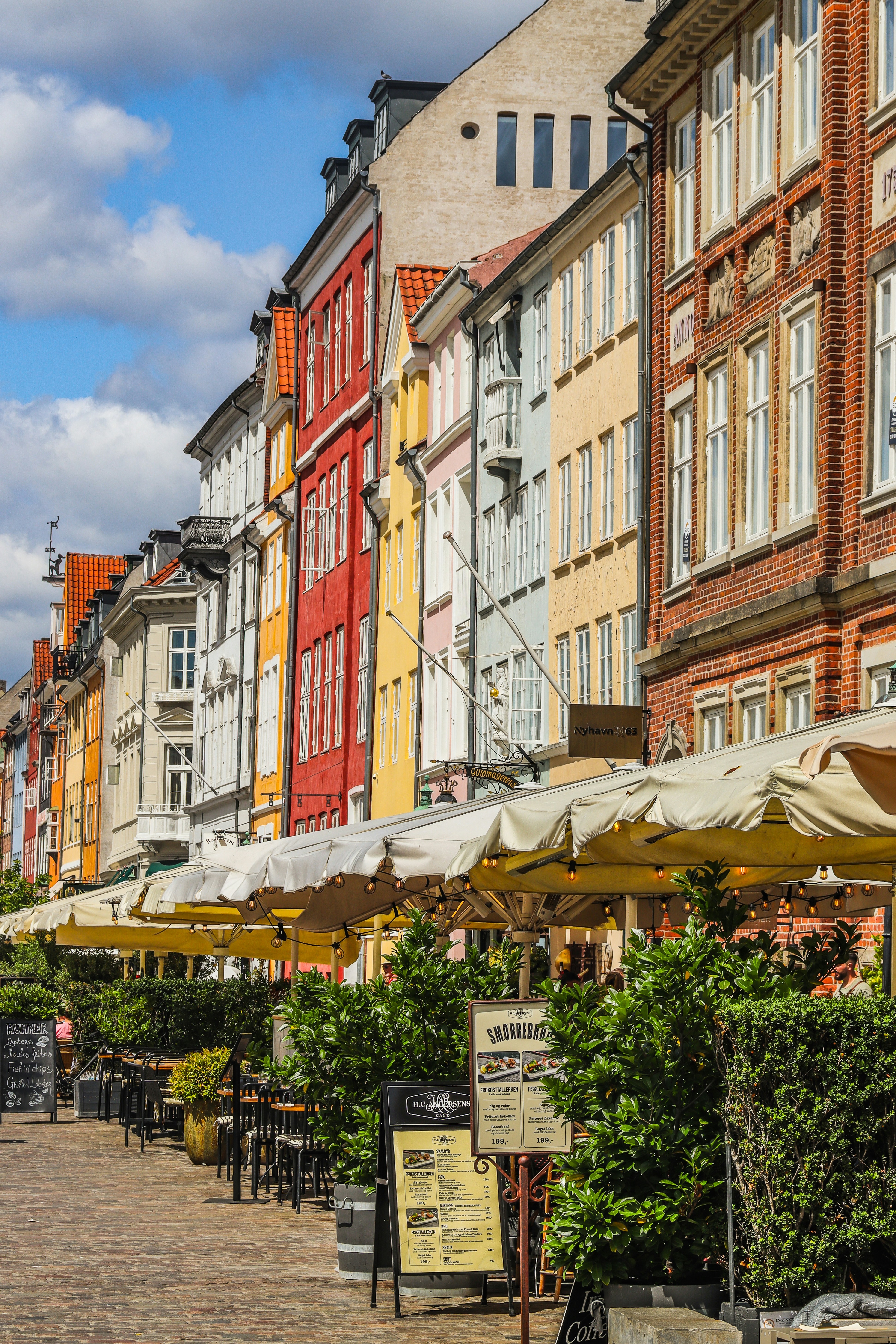 Colorful buildings along a charming Copenhagen street in Nyhavn | Colorful buildings line a sunny european street with cafes.