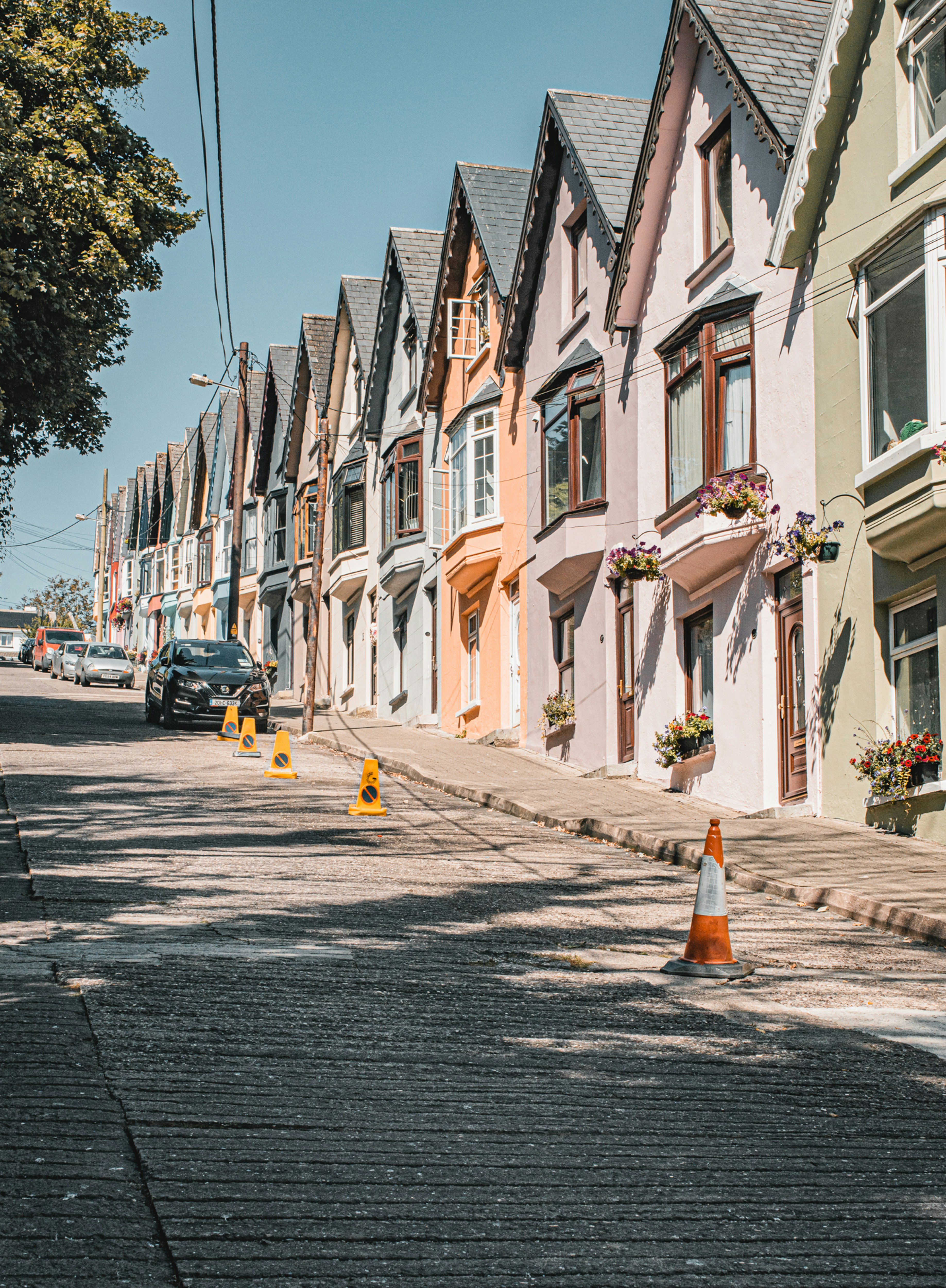 Row of pastel houses on a sunlit hill with traffic cones