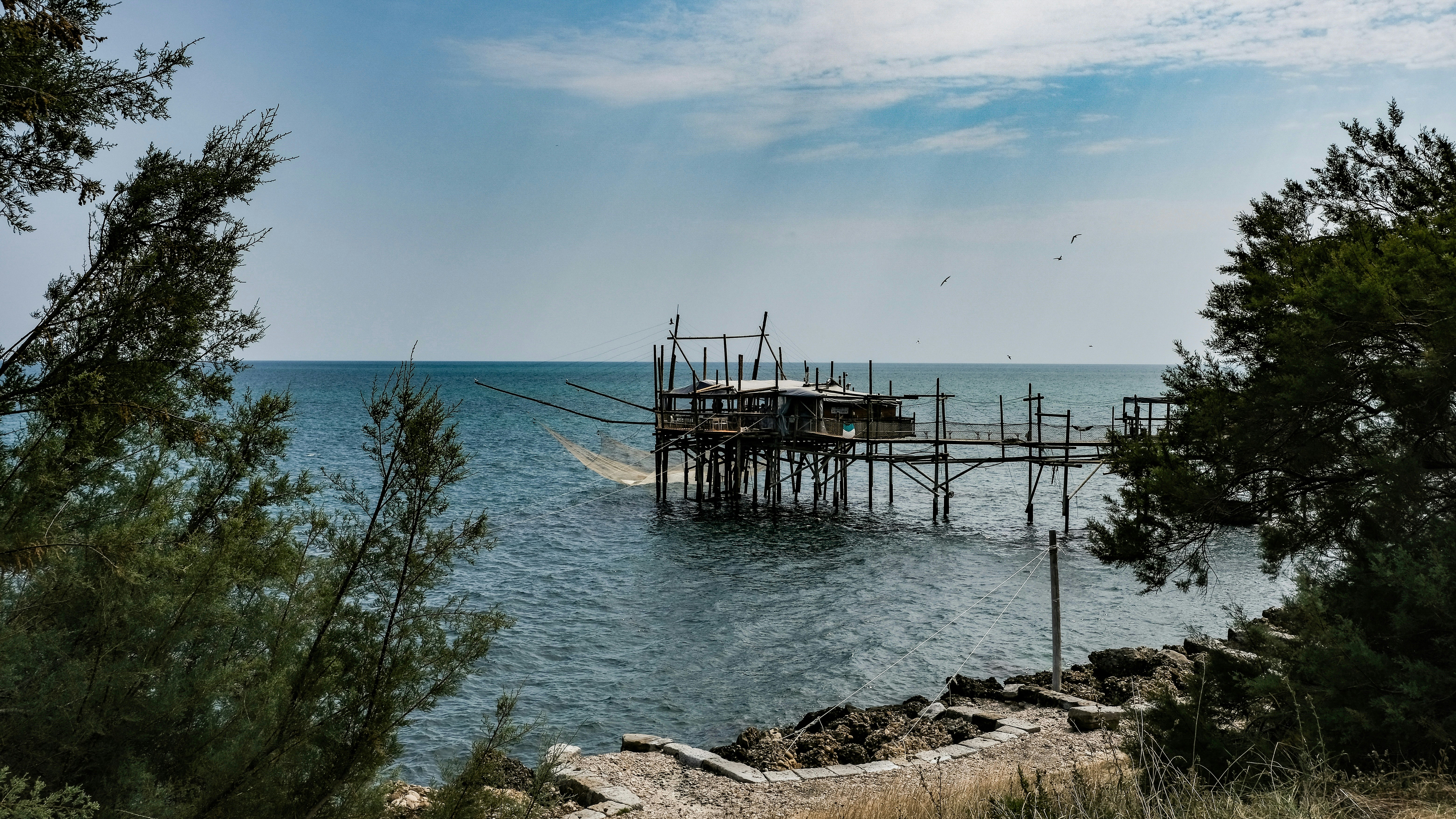 Costa dei Trabocchi, Abruzzo, Italy | Fishing structure on calm blue sea with trees