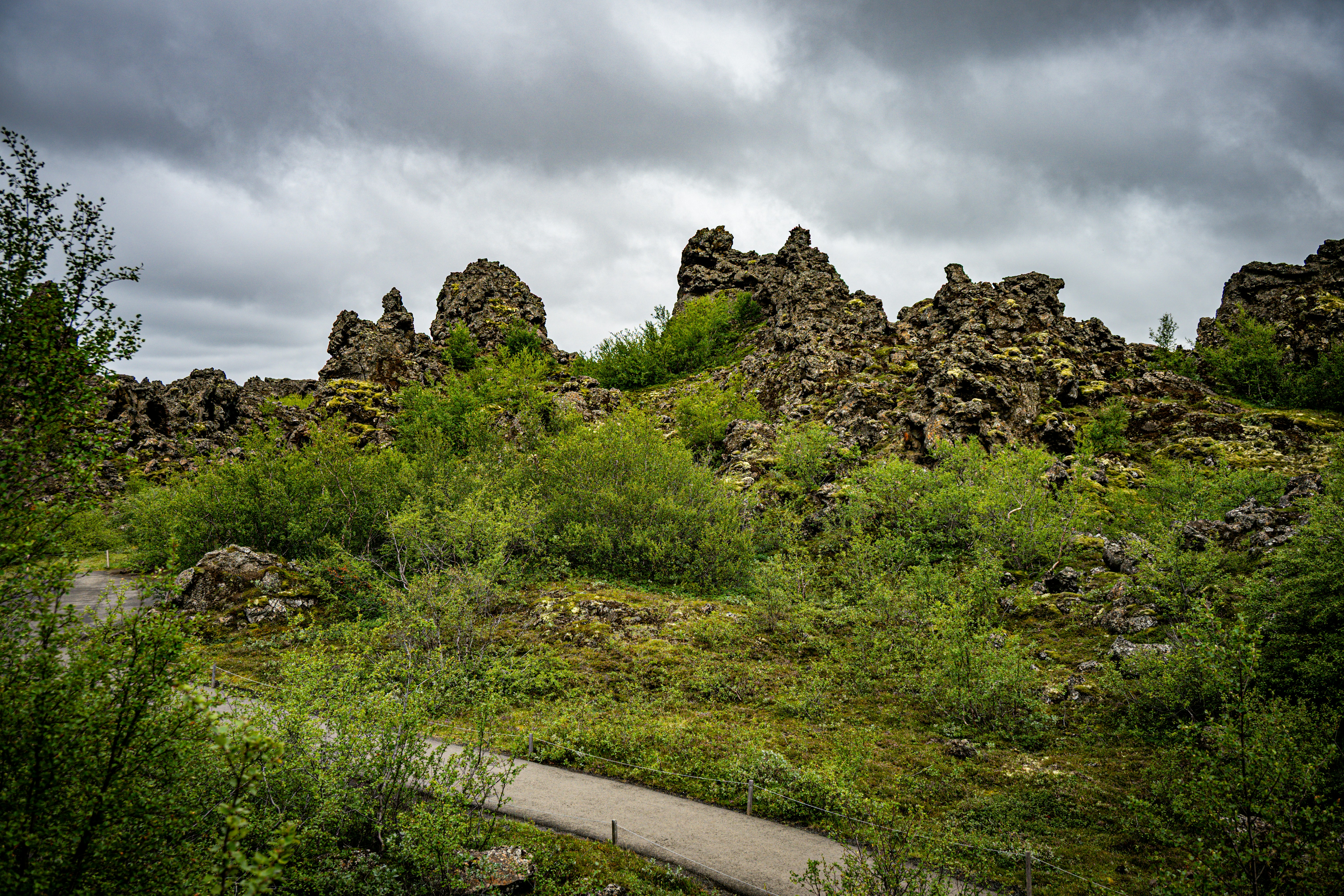 Lava rock formations rise amidst lush greenery under a moody sky, hinting at the geological history of the area.