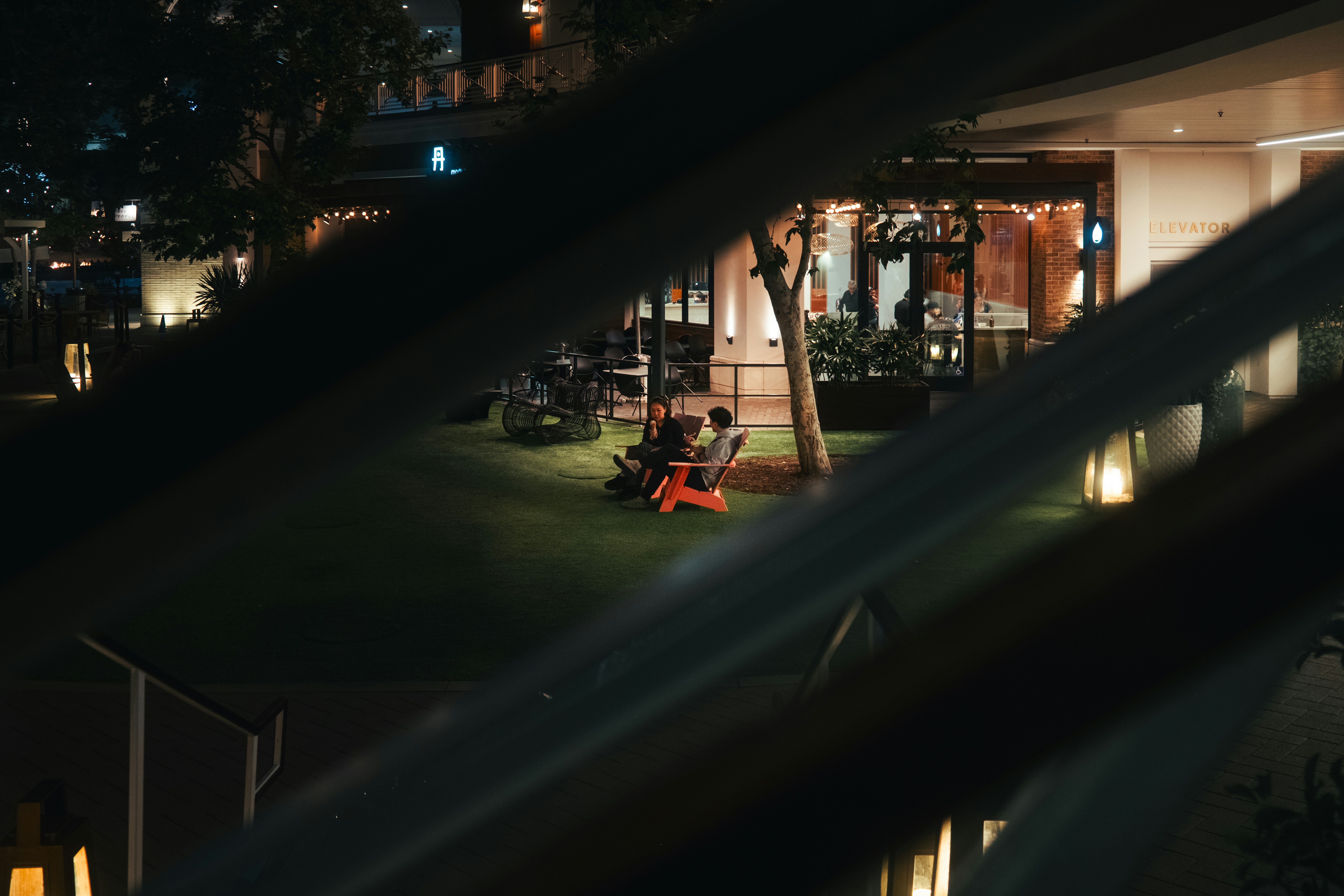 Couple sitting on a bright orange chair in a cozy outdoor setting, surrounded by soft lighting and greenery at night.