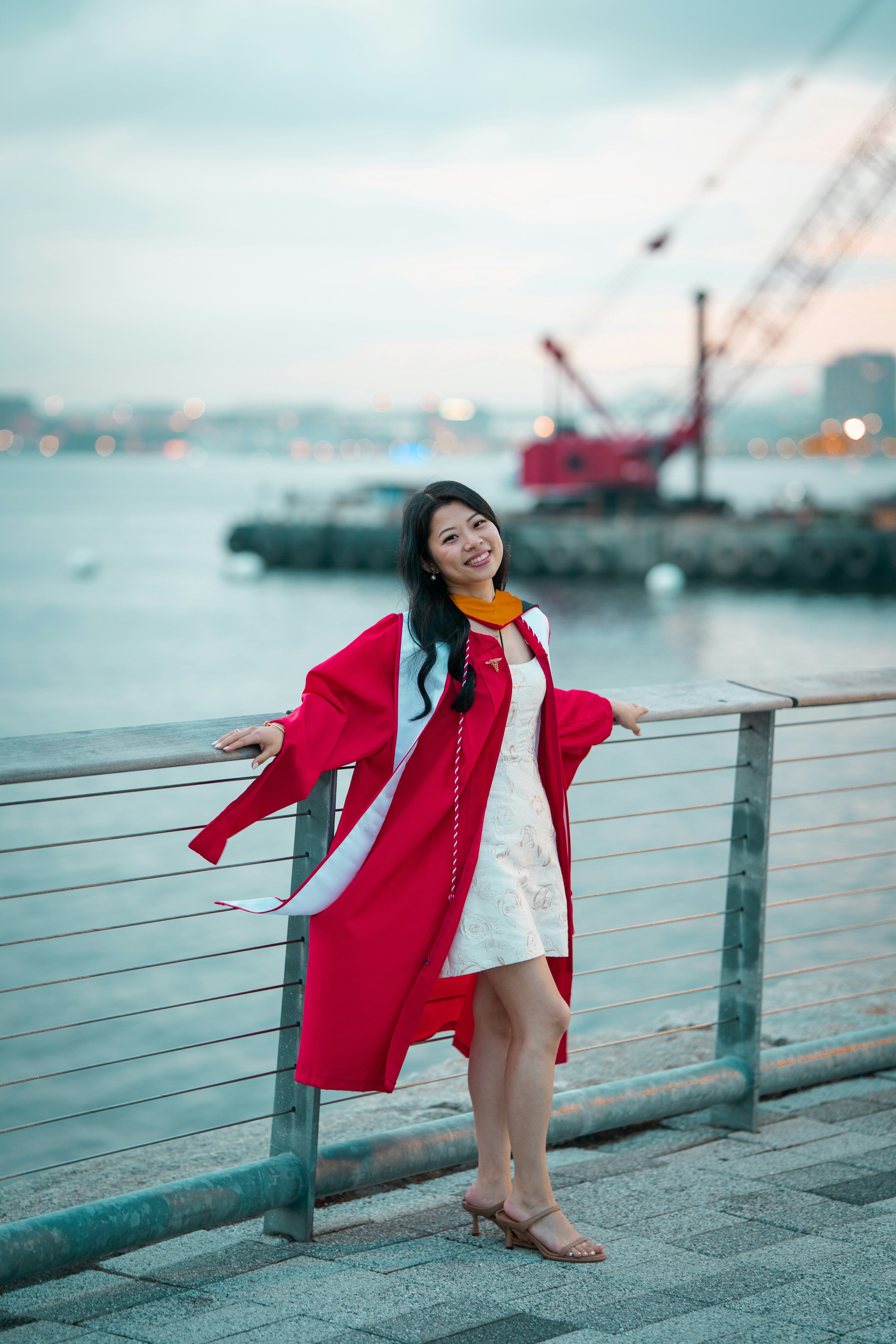 Graduation photoshoot | A smiling graduate in a red robe by the water