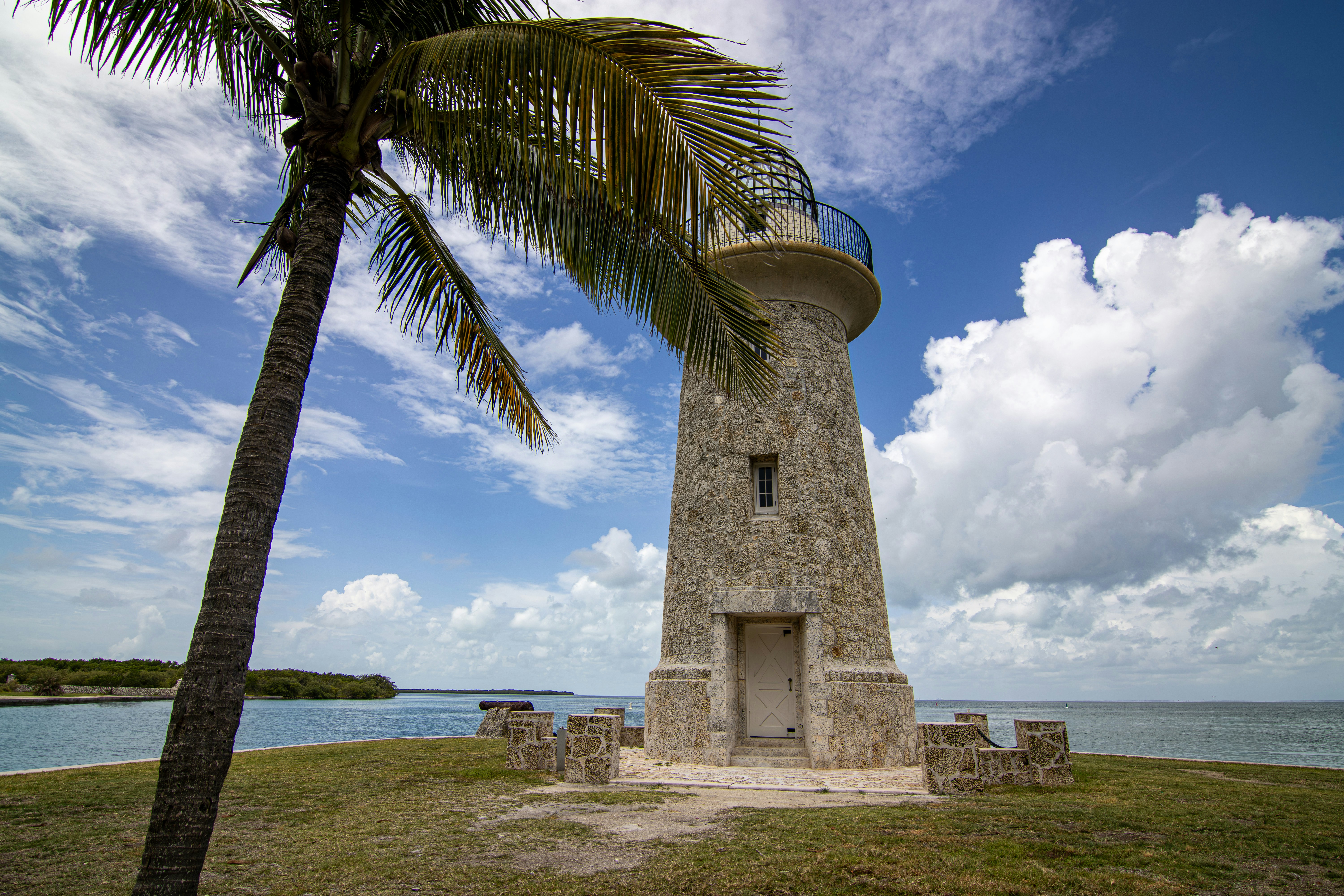 Stone lighthouse on a grassy shore with palm tree