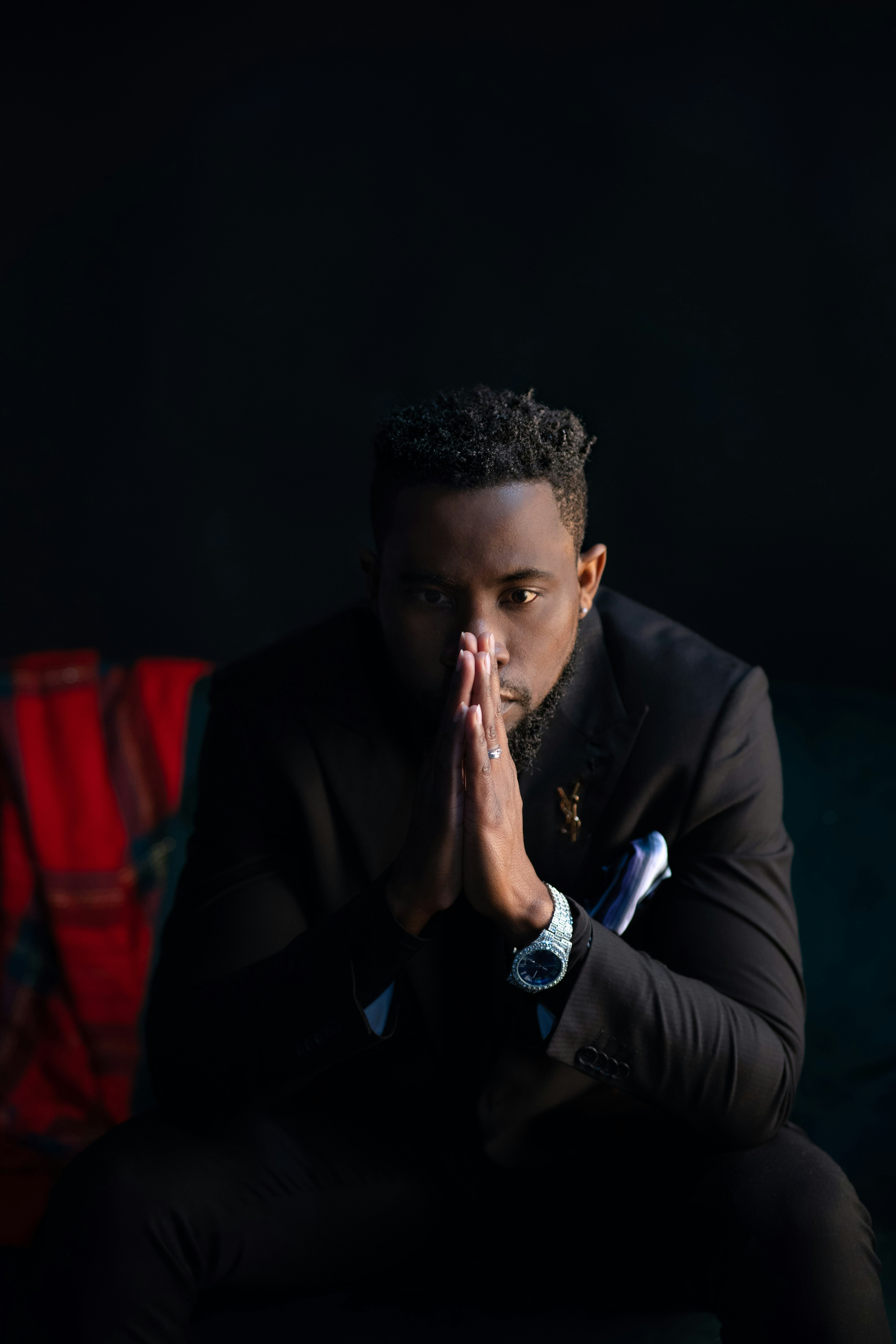 Man in a suit clasps hands in front of face.