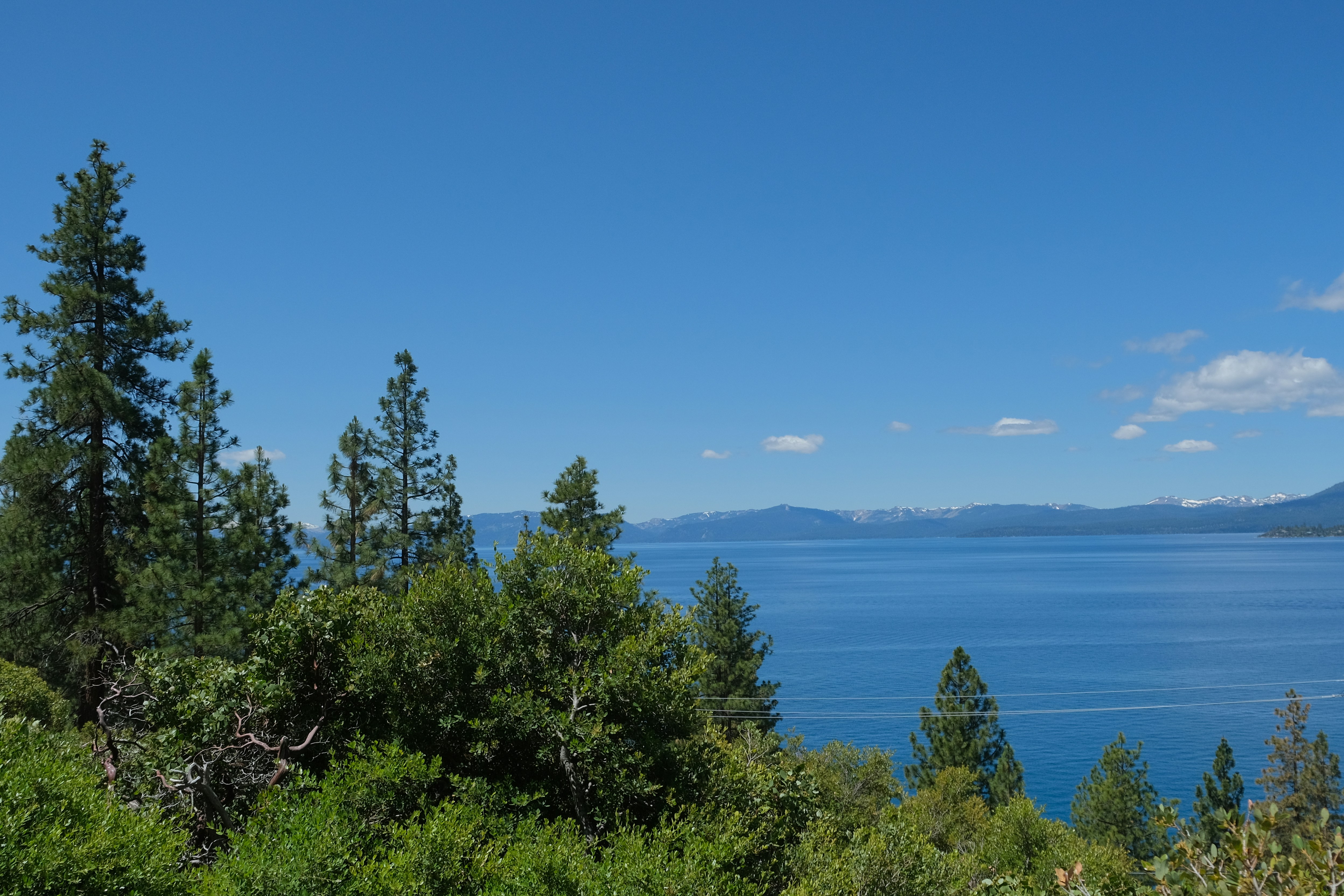 Lush greenery frames the serene waters of a lake under a clear blue sky, with distant mountains visible on the horizon.