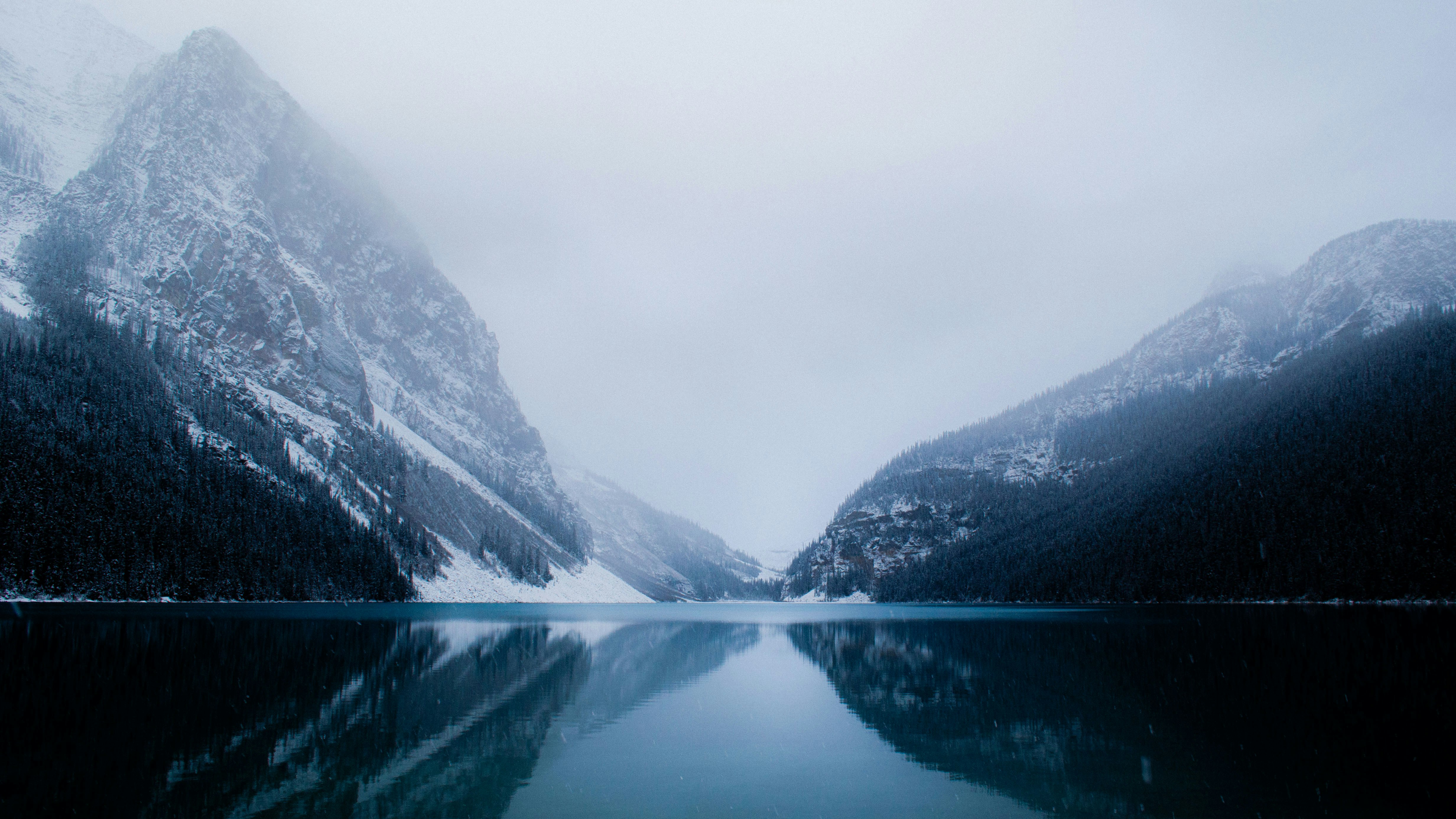 A peaceful mountain lake shrouded in mist, with towering peaks reflected perfectly on the still water, evoking serenity and majesty. | Misty mountains reflected in a calm lake