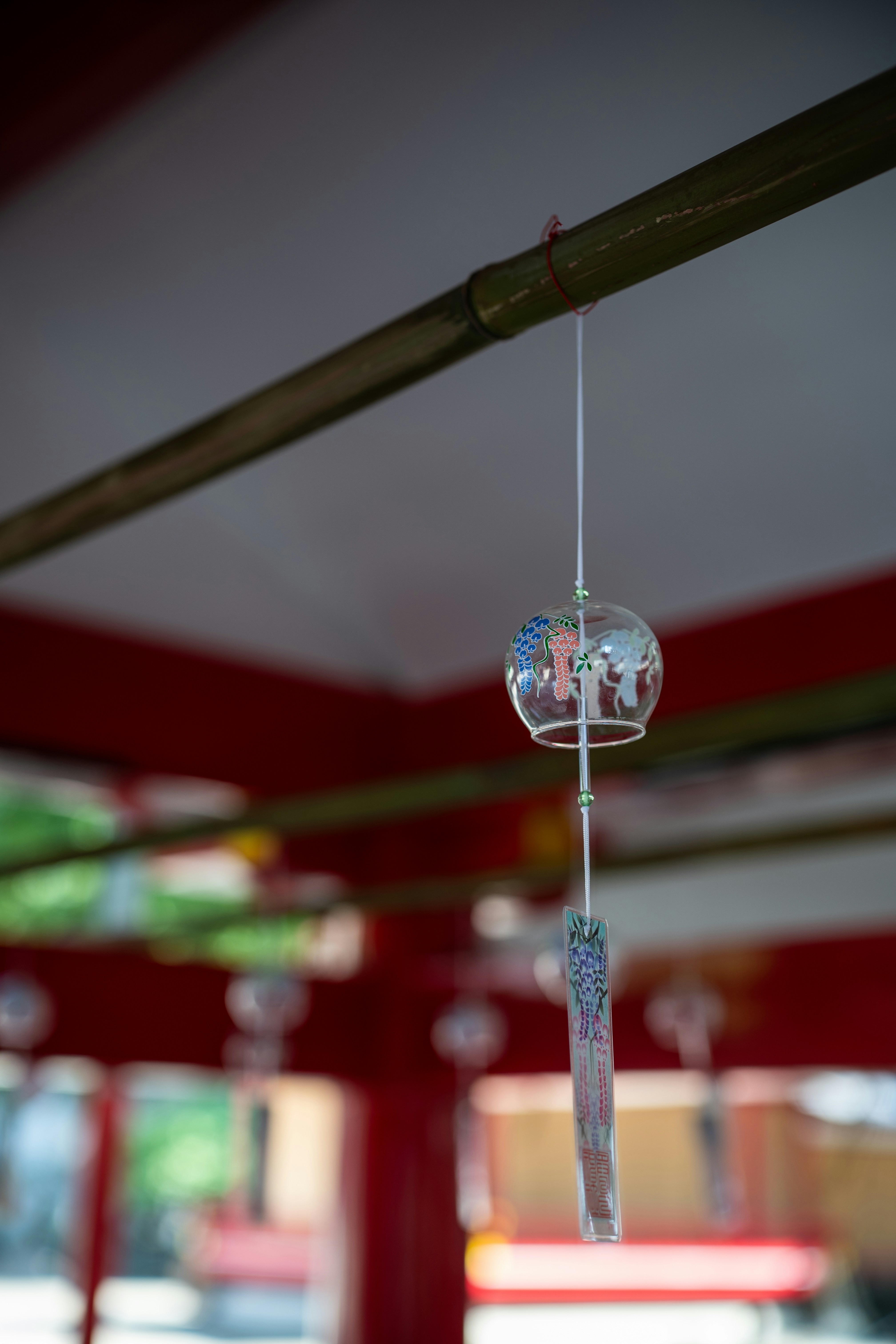 Delicate glass wind chime adorned with intricate designs, suspended from a wooden beam in a vibrant setting. The gentle breeze brings it to life.