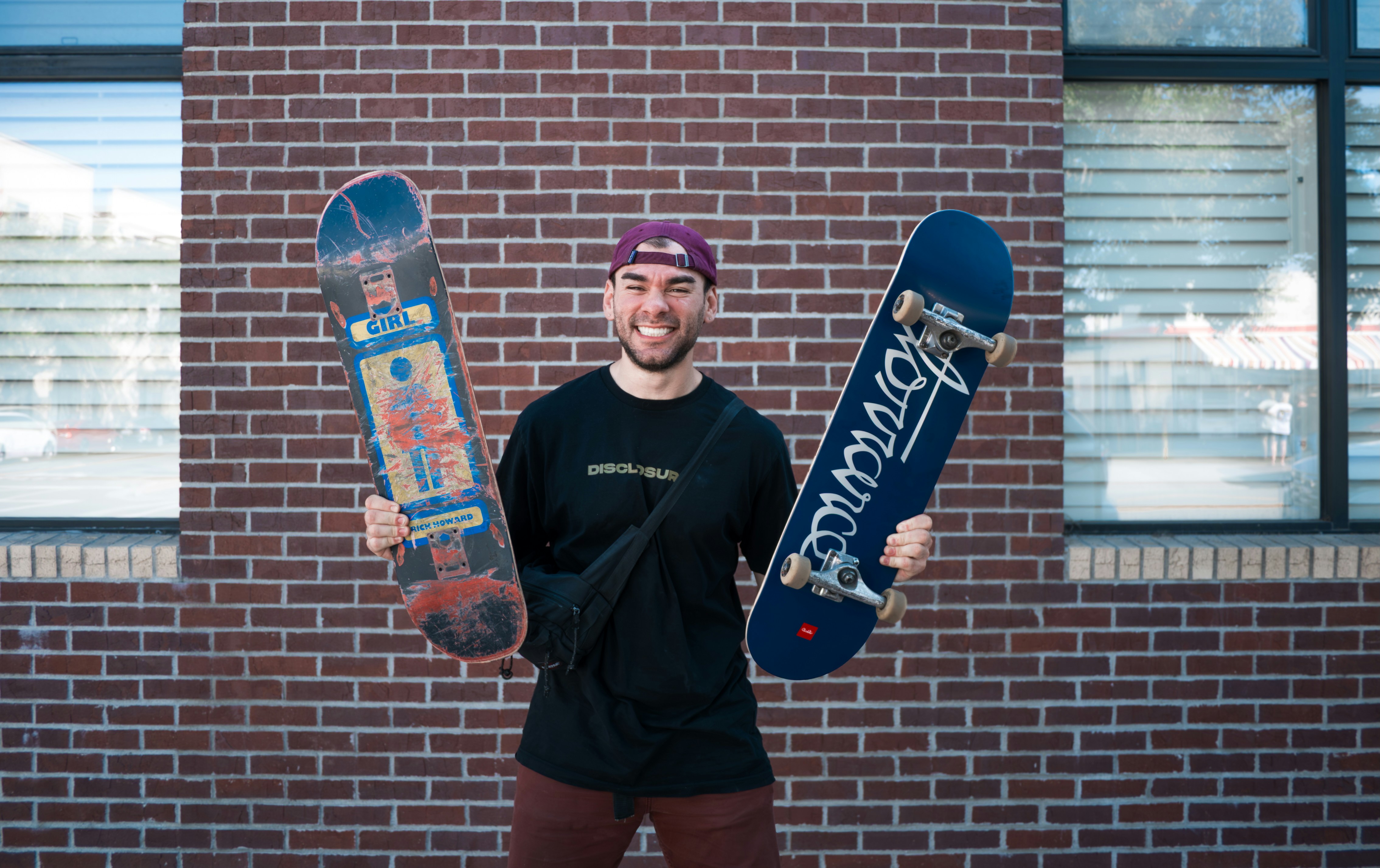 Skateboarder proudly displaying two skateboards against a brick wall, showcasing his passion for the sport.