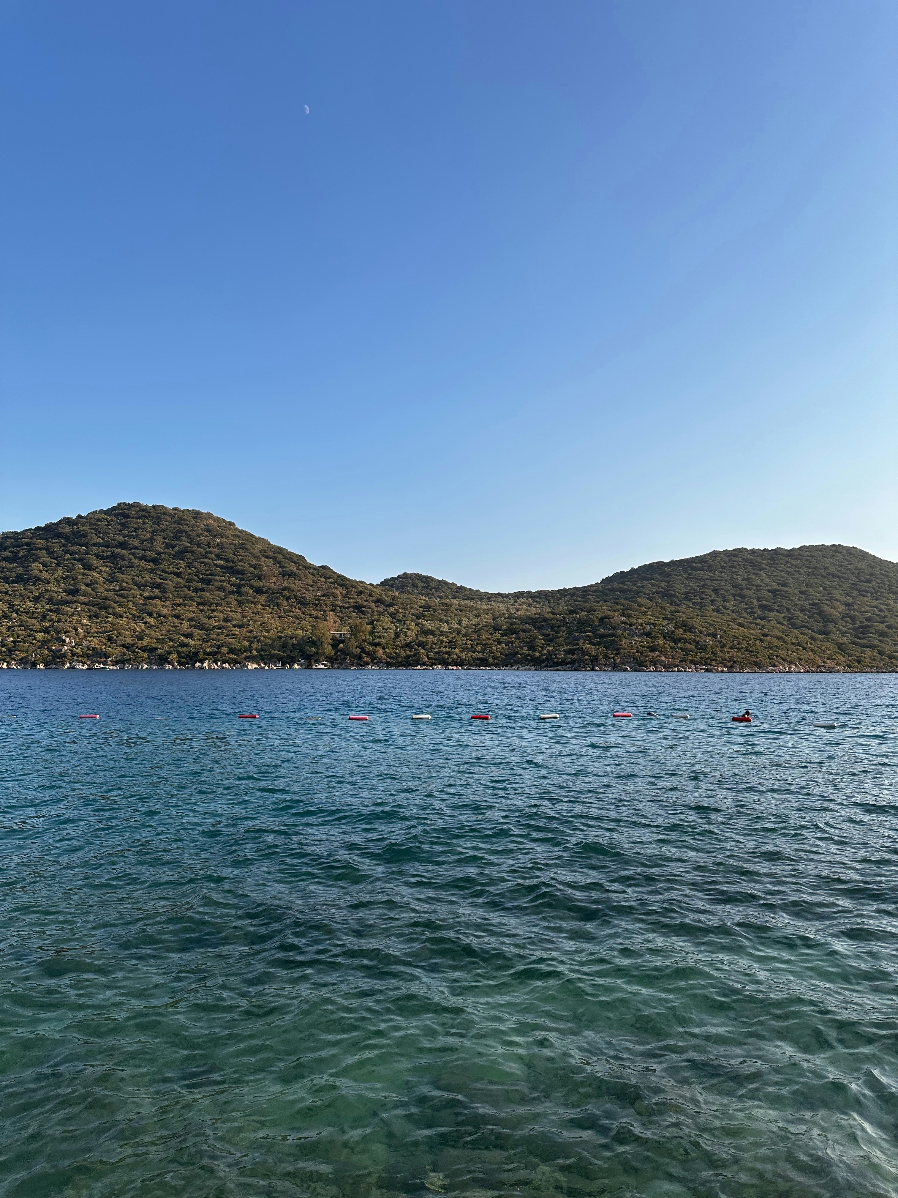 Clear blue water with green hills under a bright sky