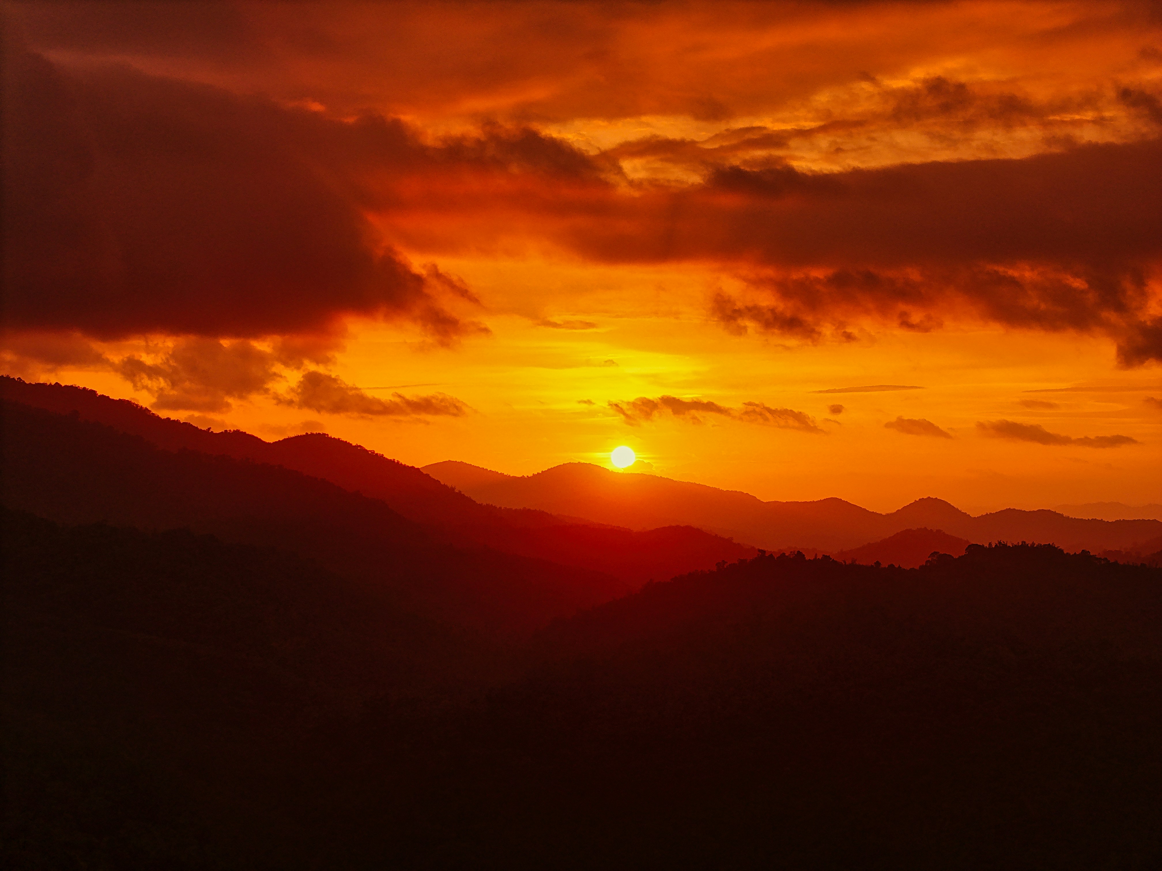 Golden sun setting behind layered mountains, casting a warm glow over the landscape. The scene captures the transition from day to night.