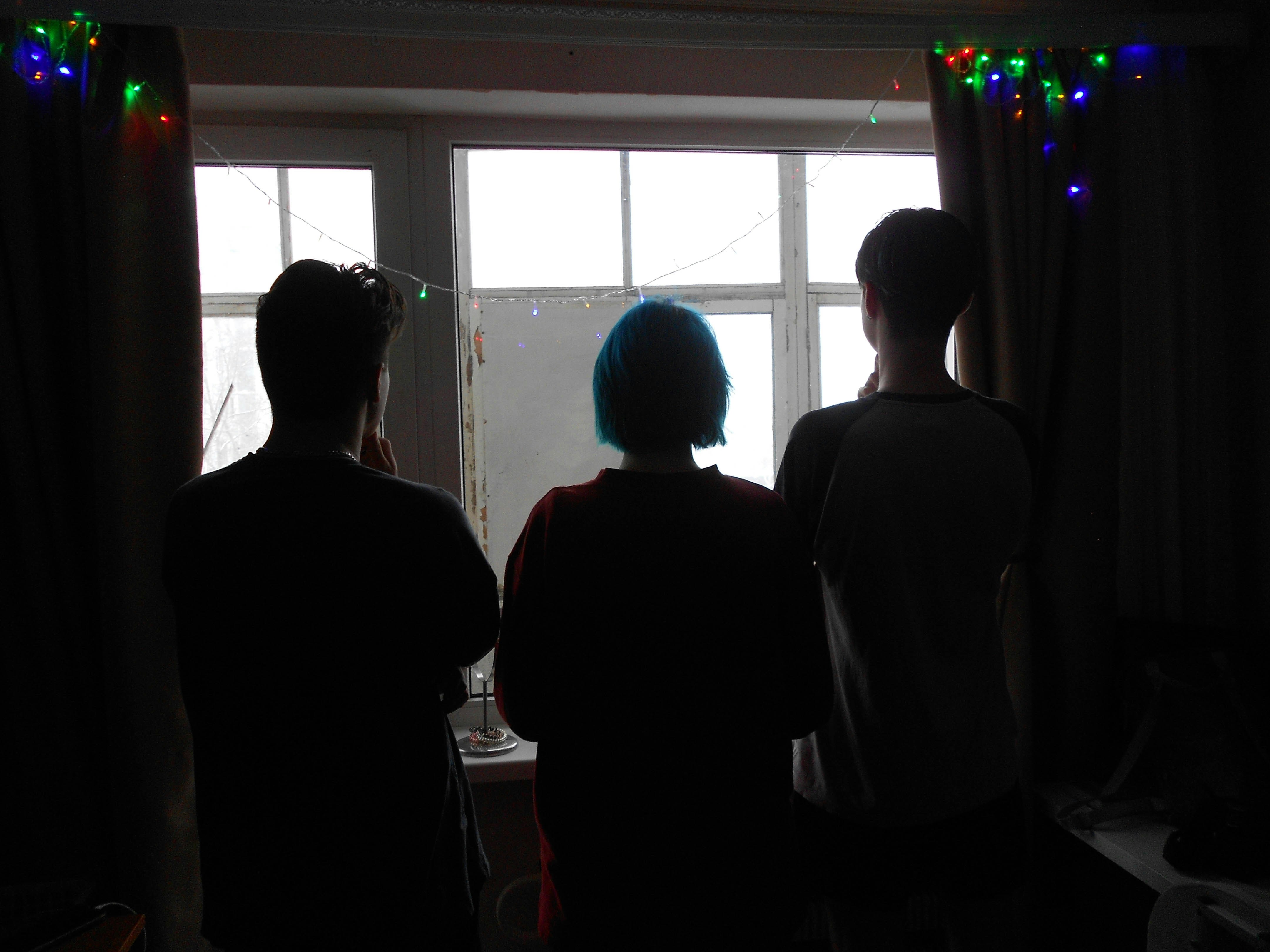 Three people looking out a window with lights.