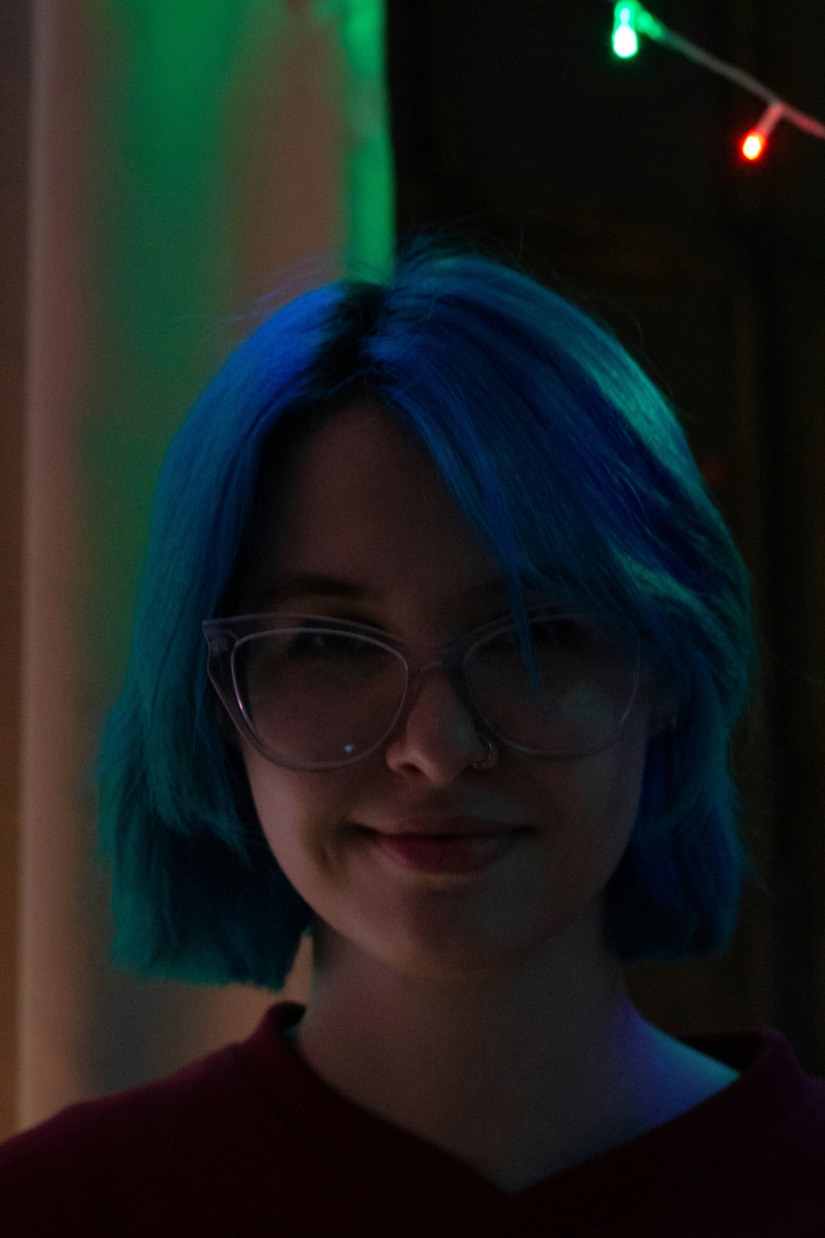 Young woman with blue hair and glasses smiling