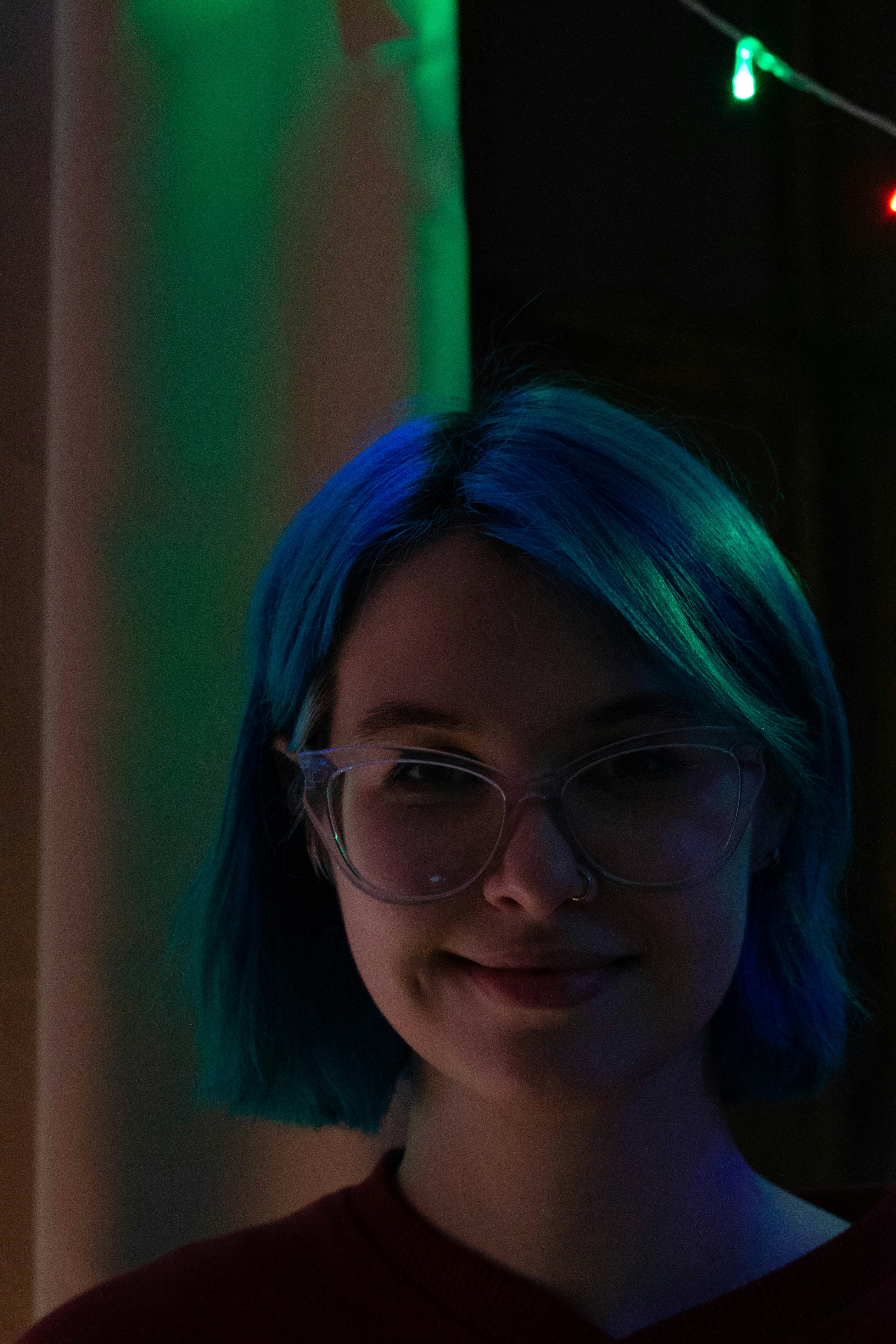 Young woman with blue hair and glasses smiling