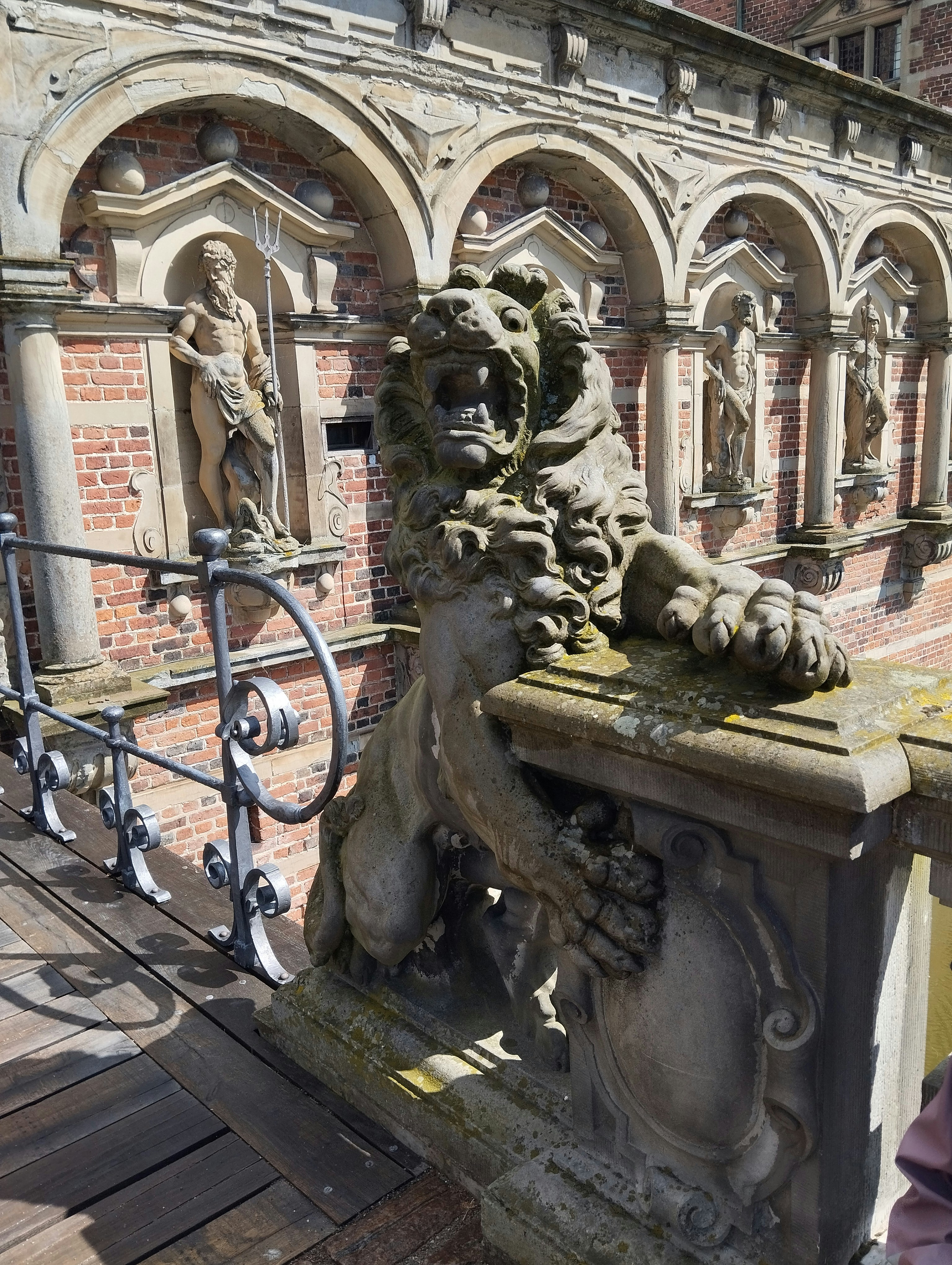 A majestic lion sculpture perched on a stone railing, overlooking intricately carved figures in a historic architectural setting.