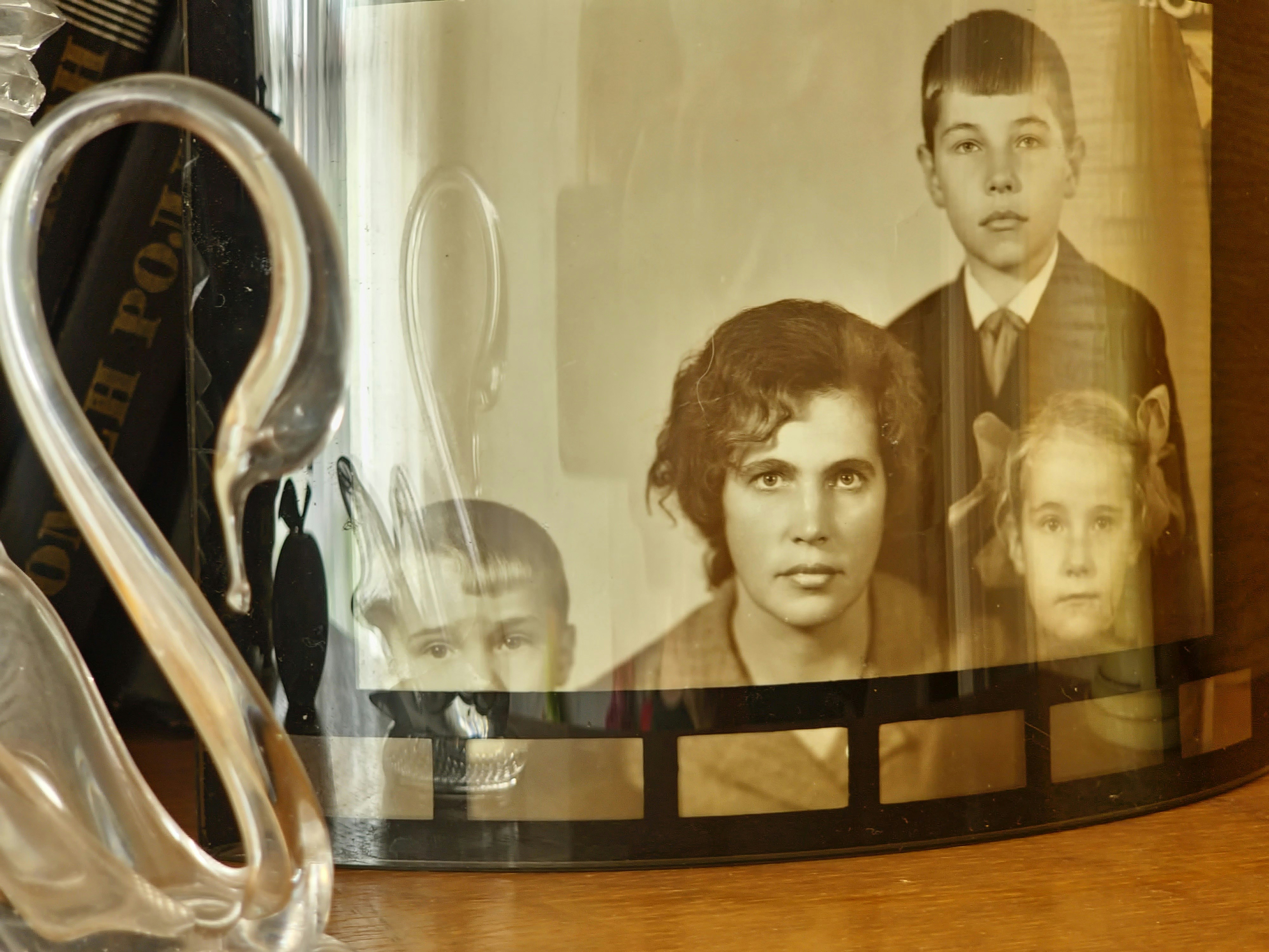The frame captures a blend of old and new: a vintage family photograph, as if frozen in time, is reflected in the facets of a modern object – a glass swan. The play of light and reflections creates layers, immersing the viewer in an atmosphere of memories and nostalgia. | Vintage family portrait on a glass surface.