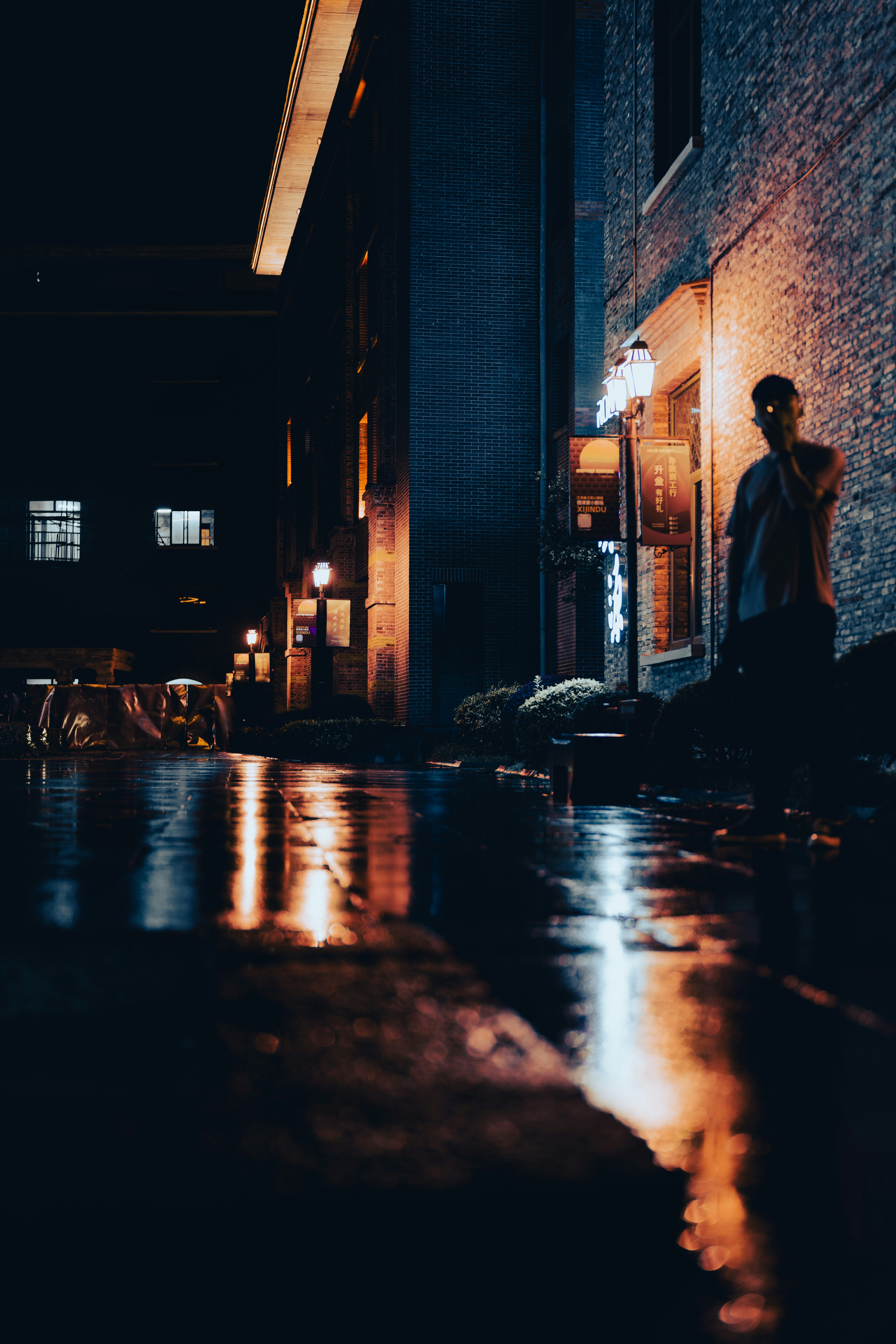 A dimly lit urban alley glistening with rain, featuring warm lamplight and a solitary figure in contemplation.