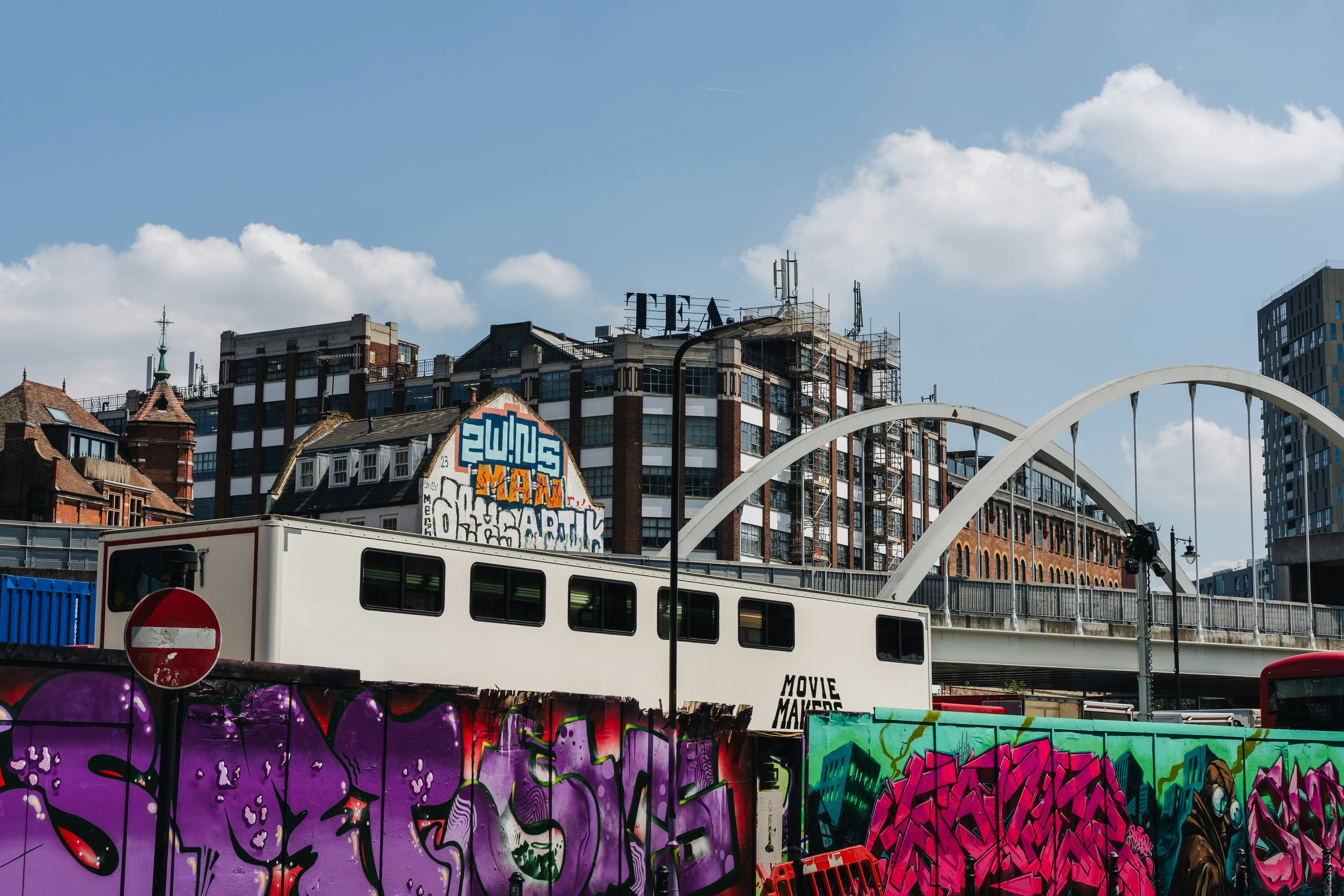 Graffiti art covers a wall in front of buildings and a bridge.