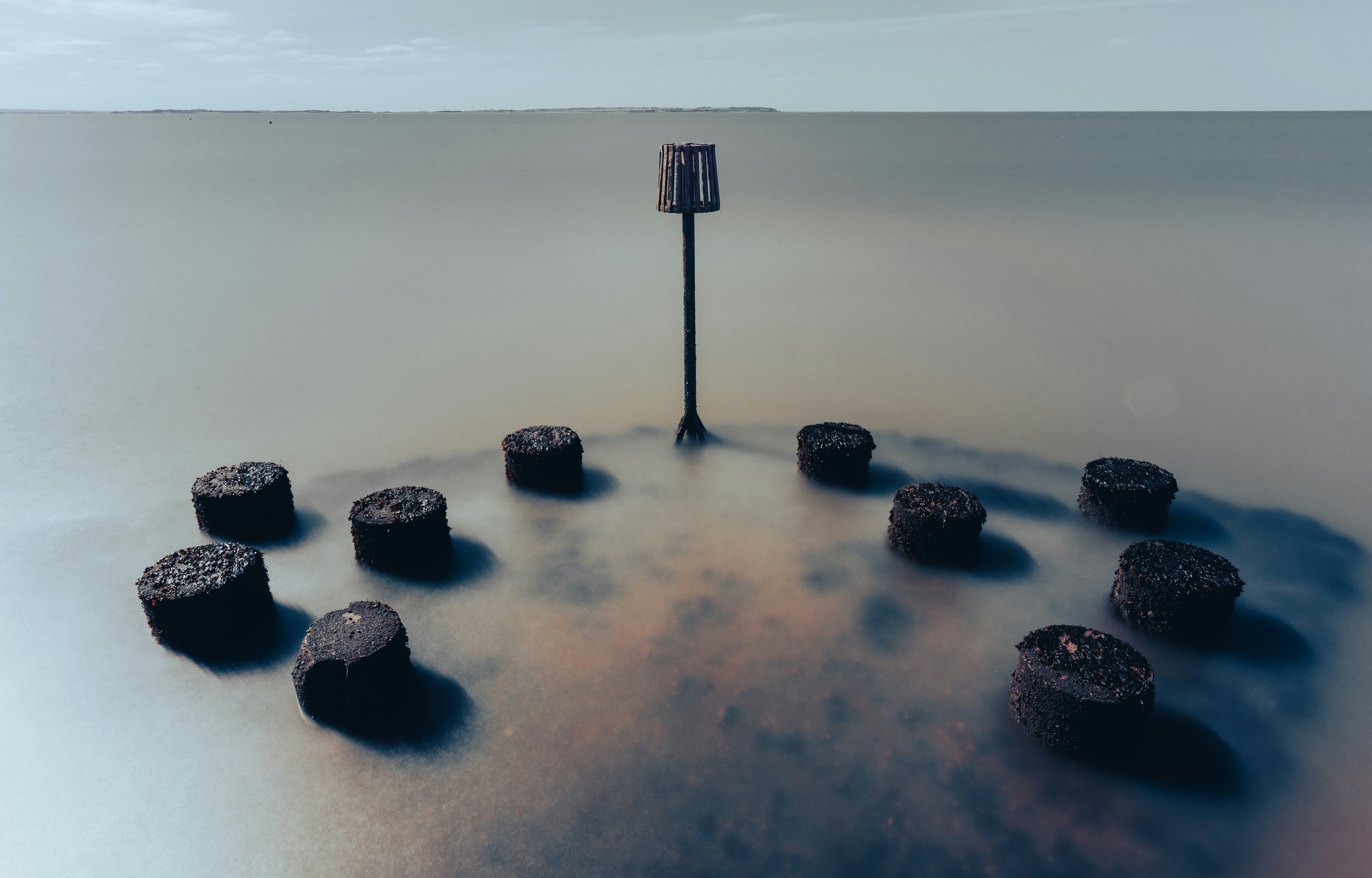 Sharp concrete against the soft sea | Wooden posts arranged in a circle with a marker.
