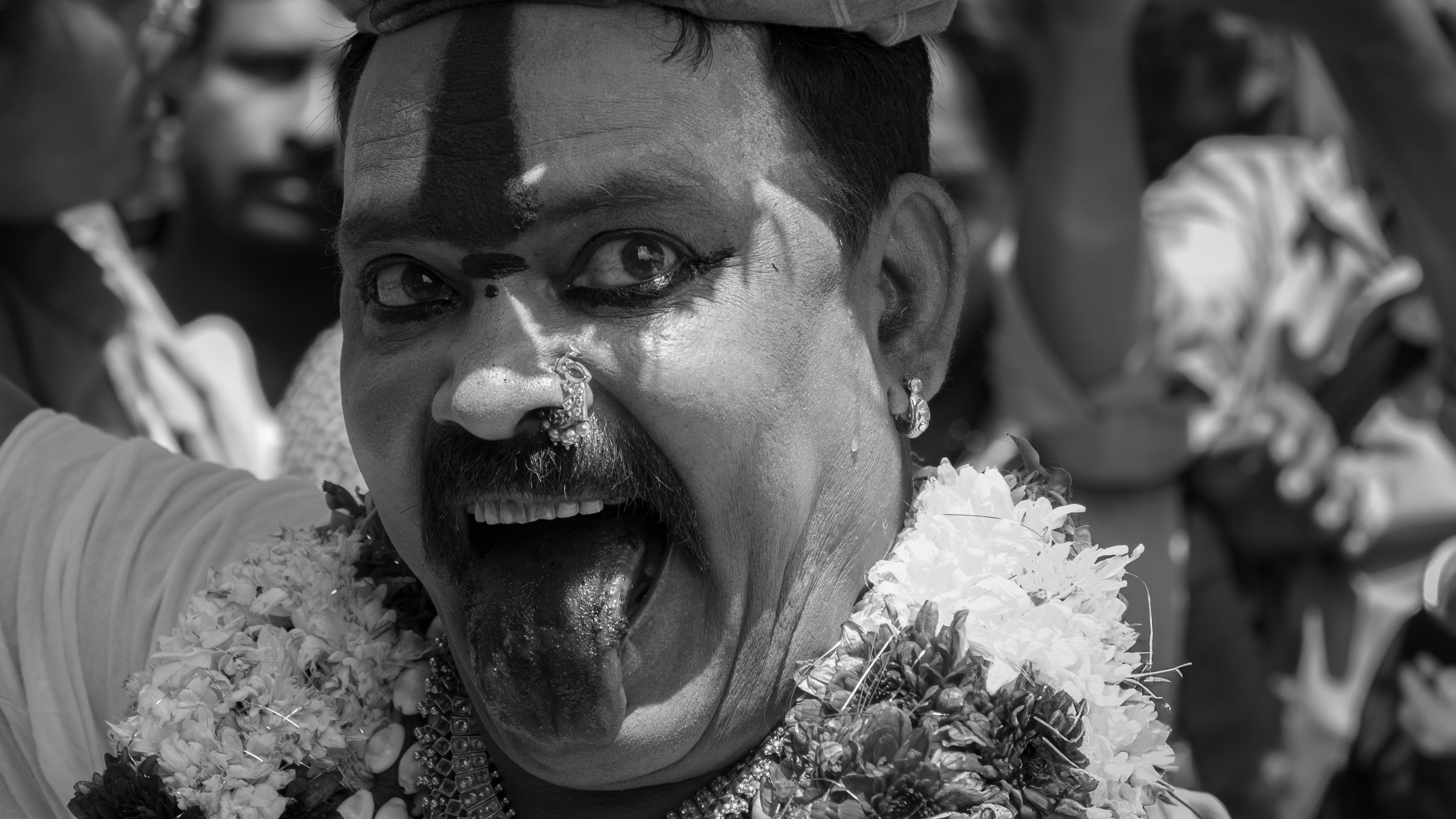 A man adorned with floral garlands and dramatic face paint expresses fervor during a cultural celebration, showcasing rich traditions and emotional depth.