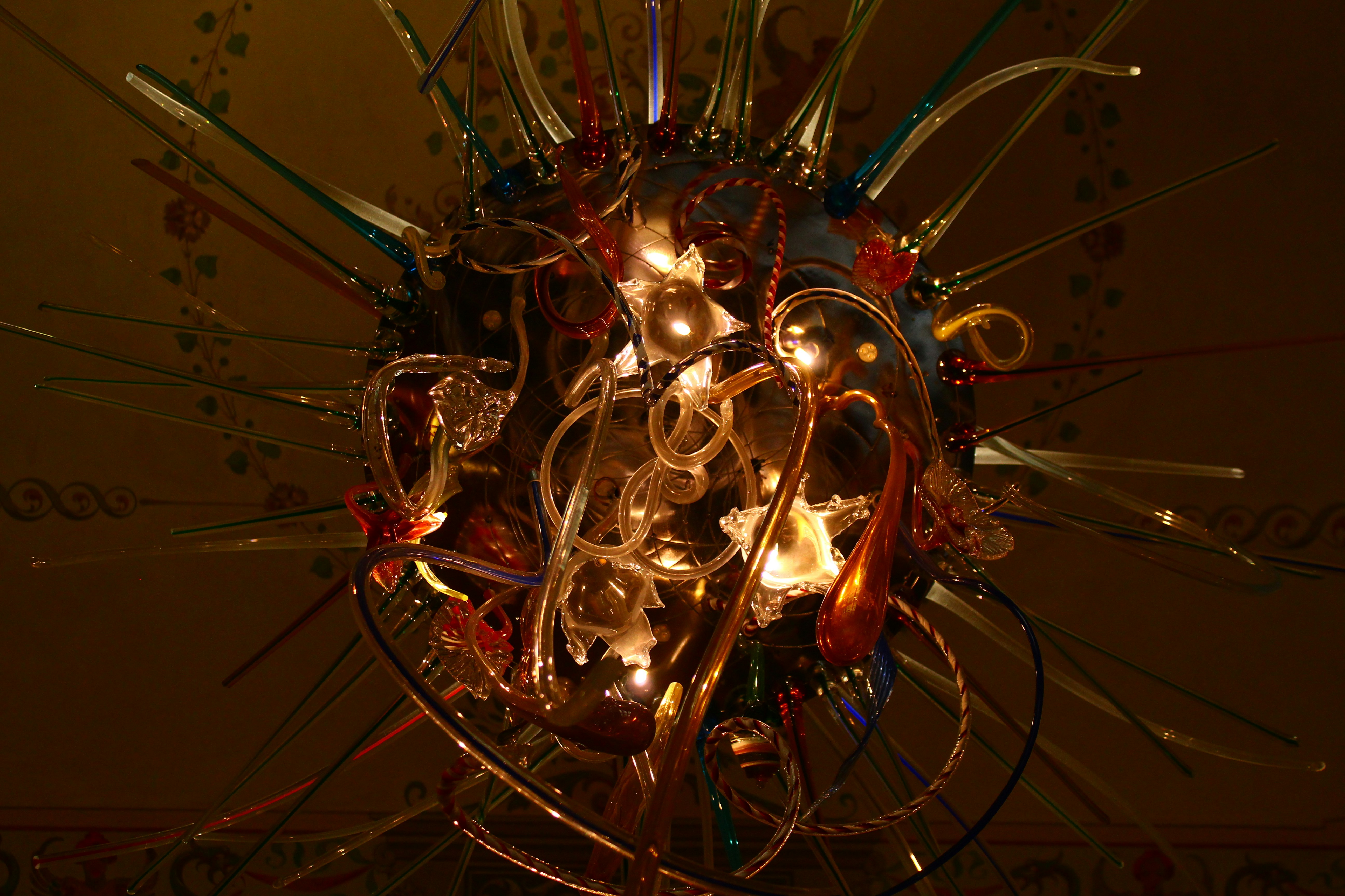 Intricate glass chandelier with vibrant colors and swirling shapes, casting a warm glow in a dimly lit space.