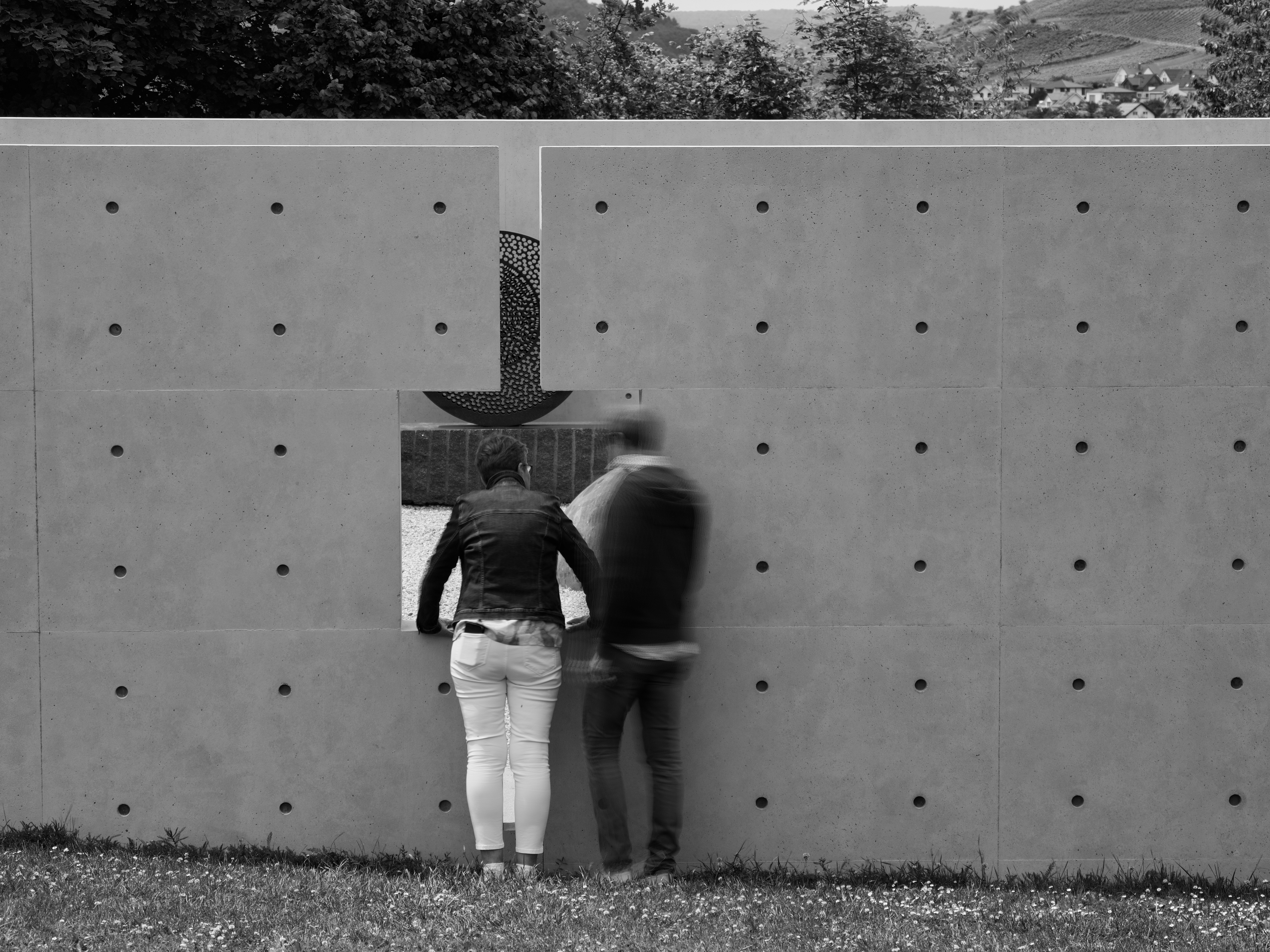 Two people look through a concrete wall opening.