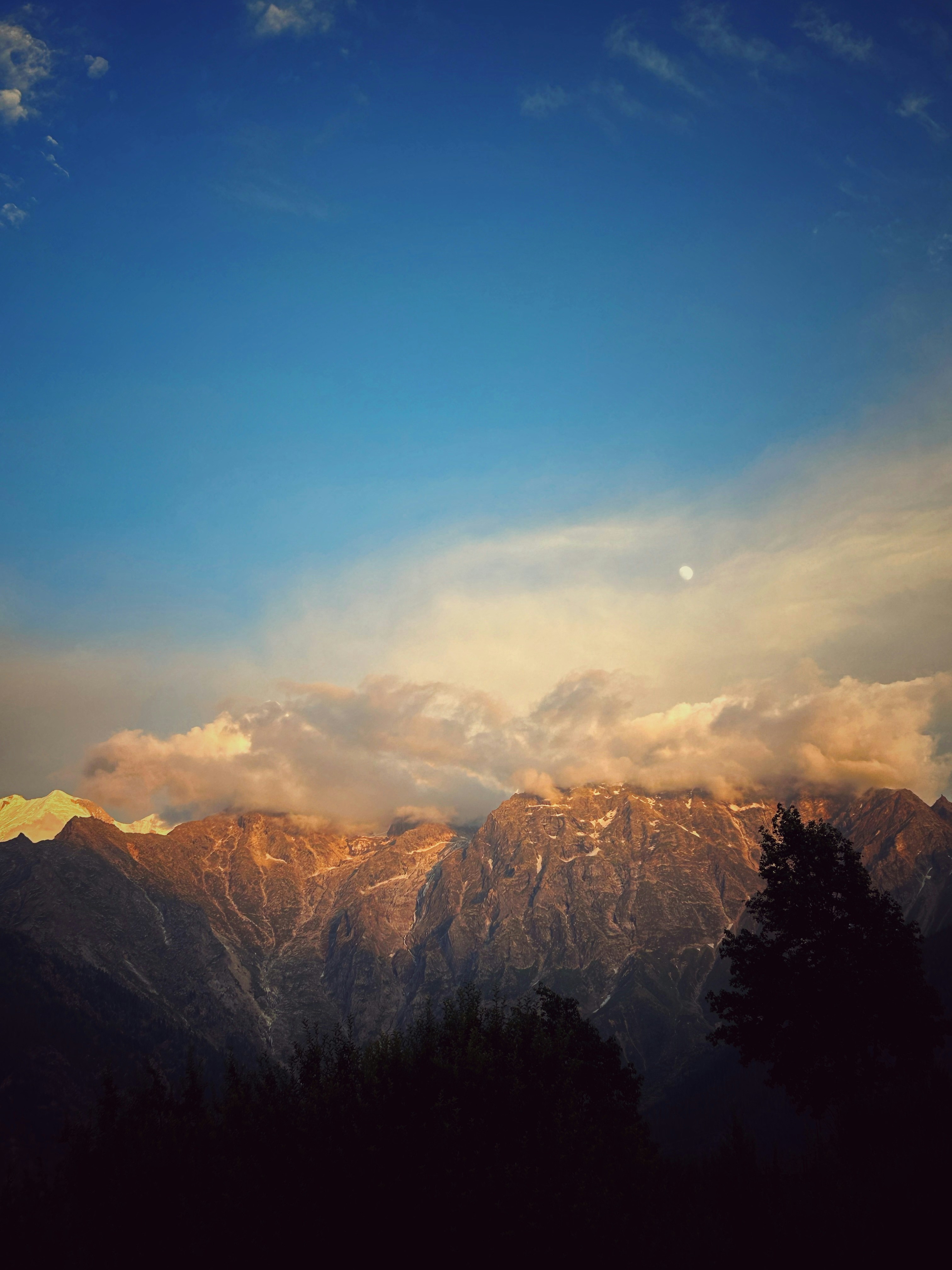 Sunlit mountain peaks with clouds under blue sky