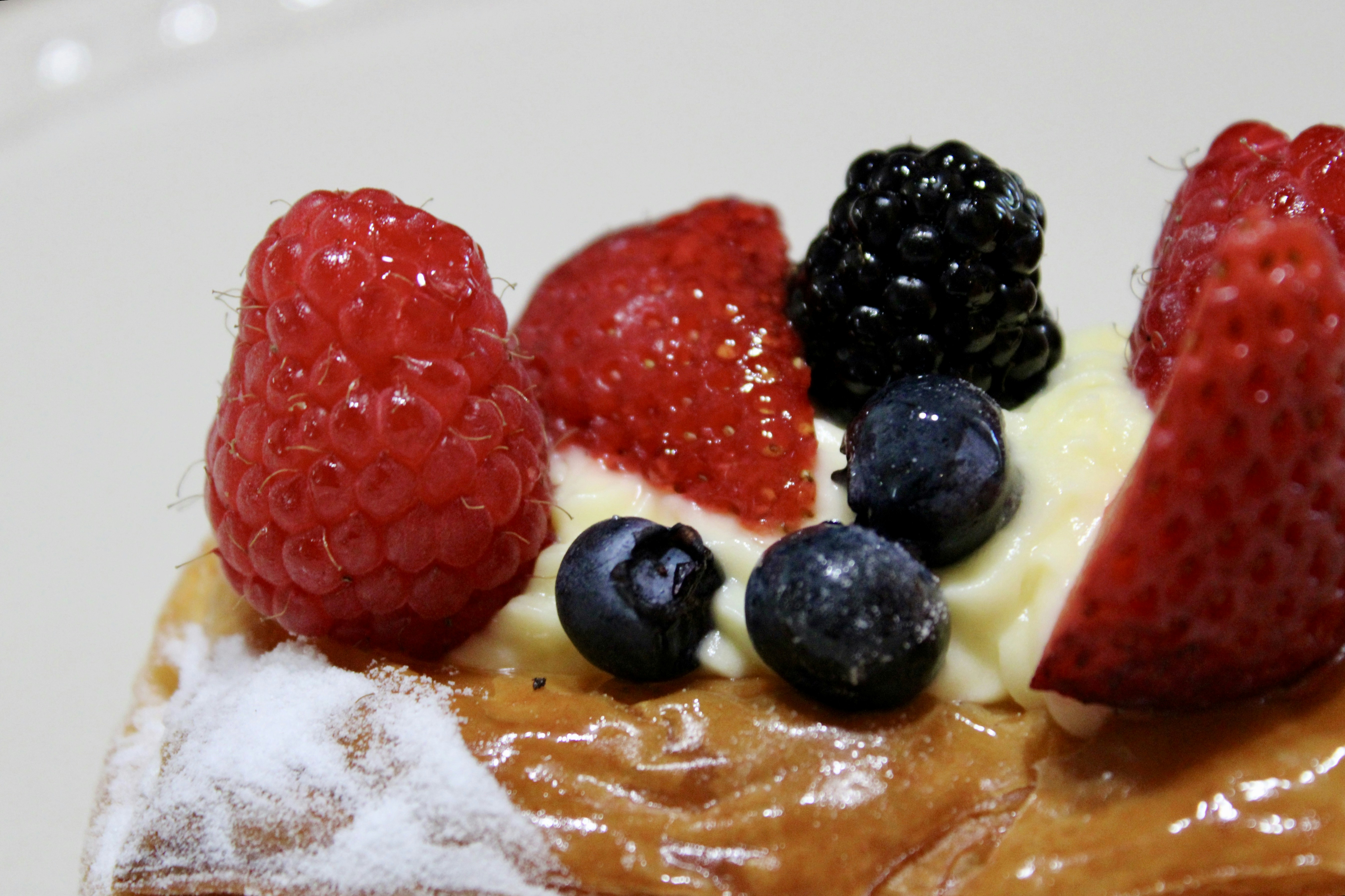 A delectable pastry topped with an assortment of fresh raspberries, strawberries, blackberries, and blueberries, showcasing a creamy filling. 