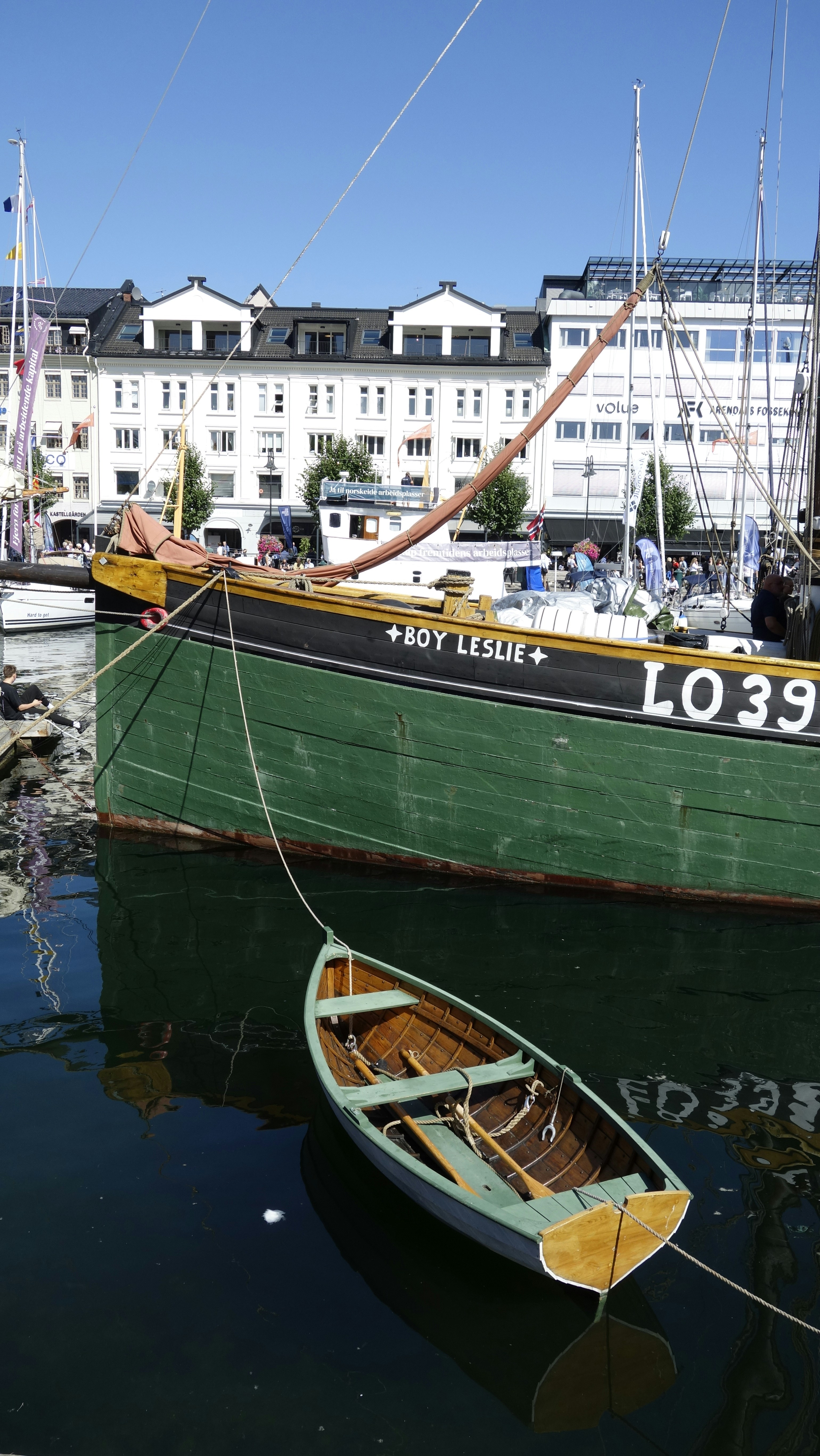A small boat tied to a large green boat in harbor.