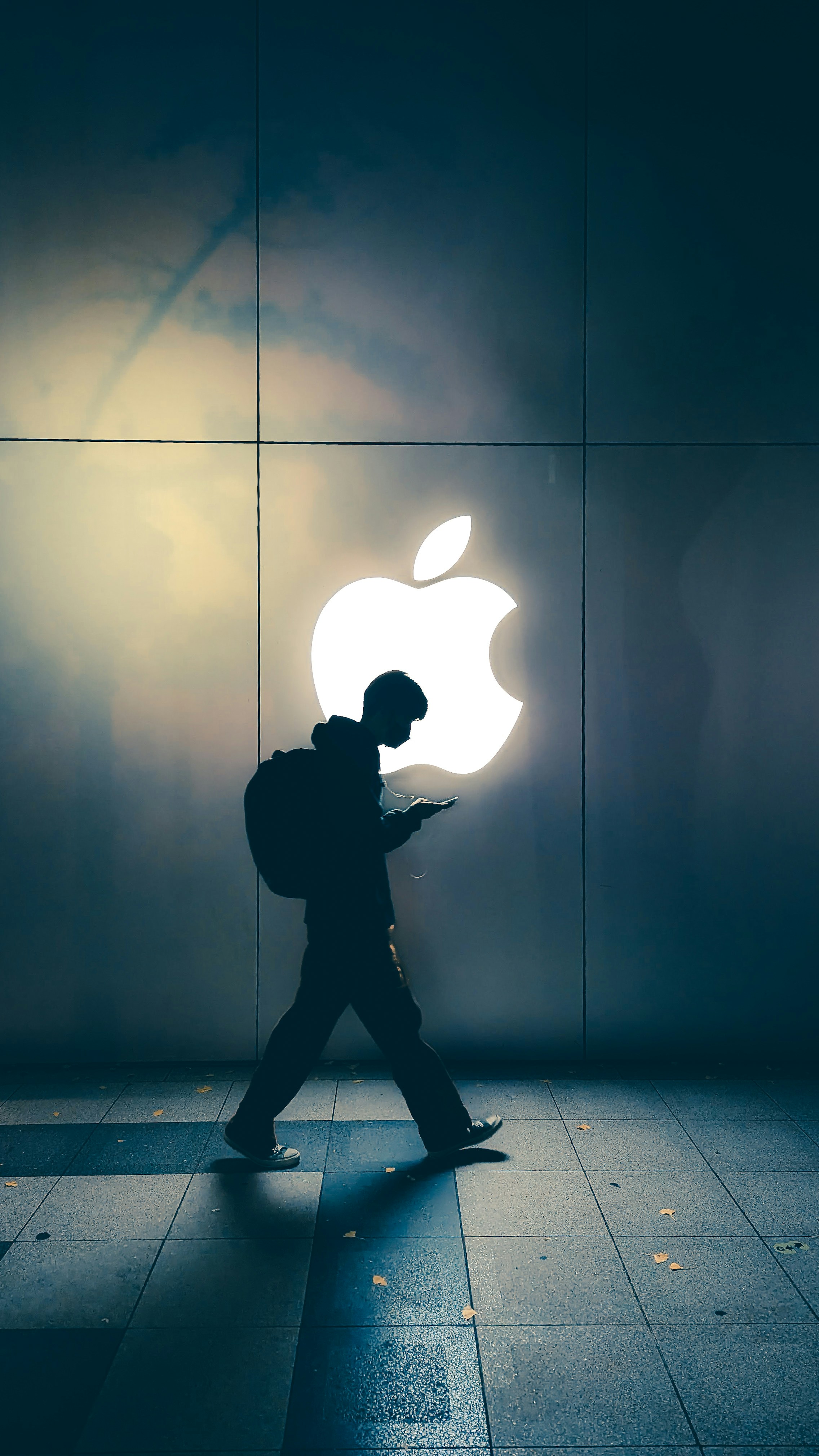 Person walks past illuminated apple logo at night.