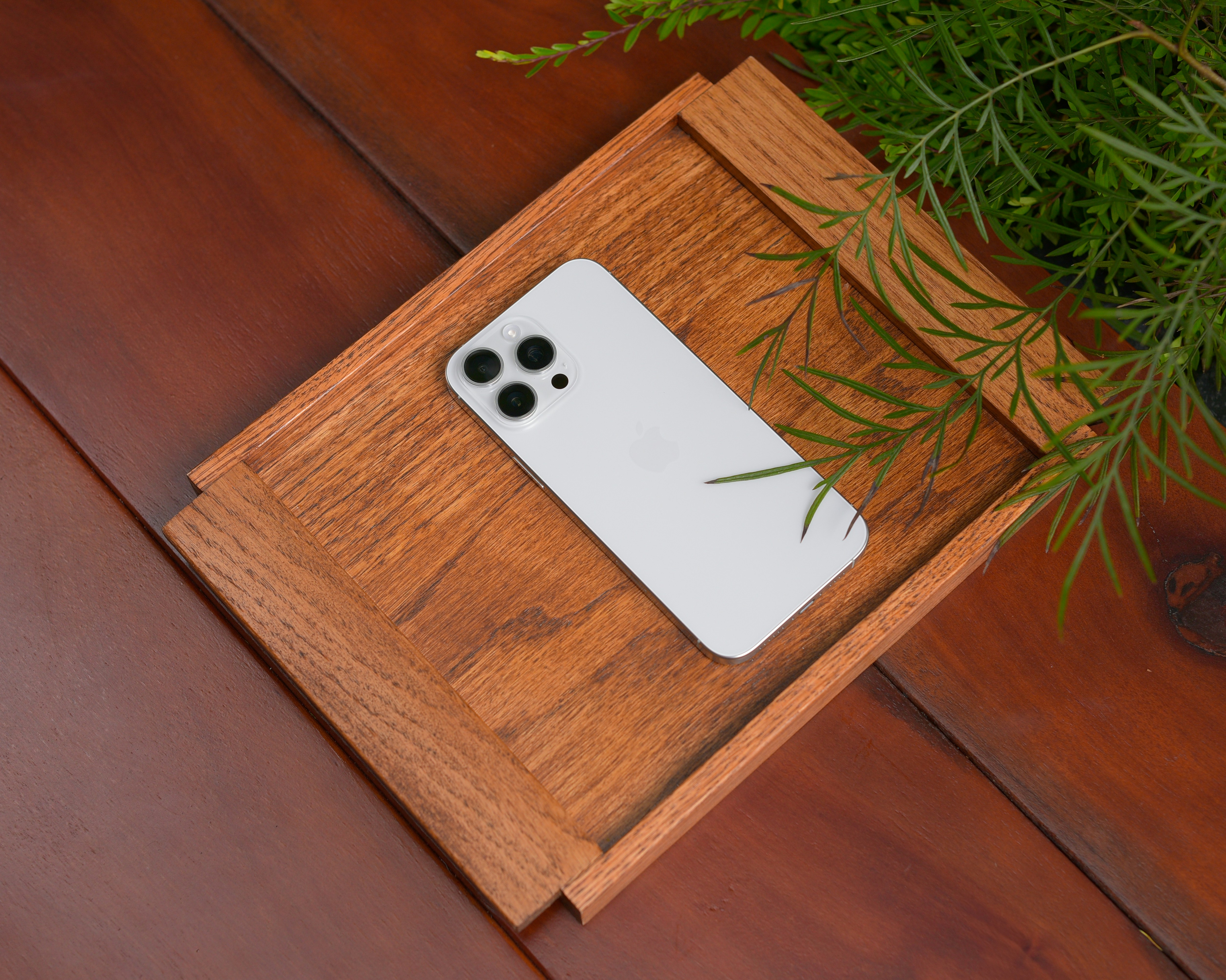White smartphone resting on a wooden tray, surrounded by green foliage, creating a serene and organized aesthetic.