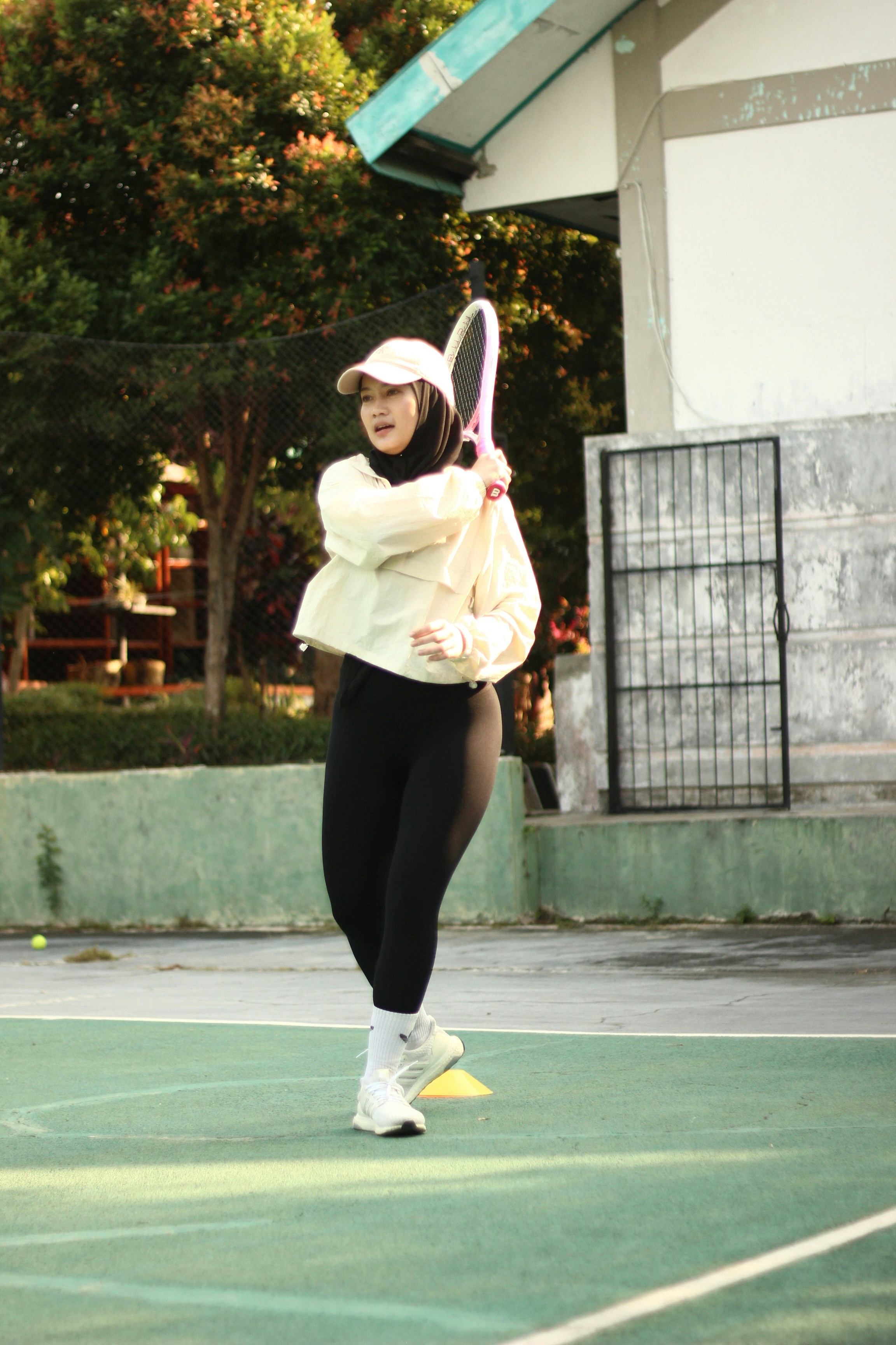 Woman in hijab playing tennis on a court.