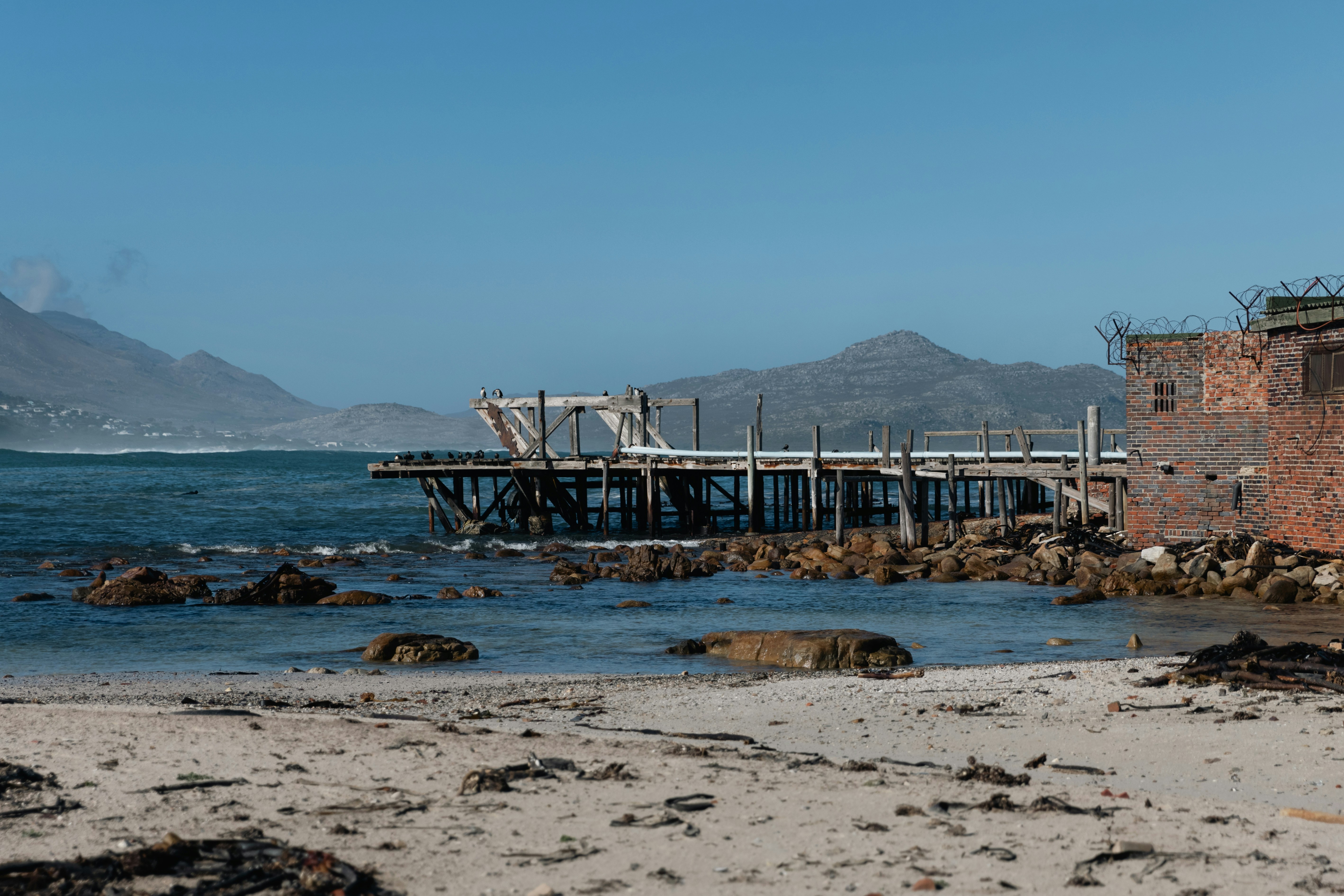 Abandoned pier along the Atlantic Ocean. | Old wooden pier on a rocky shore with mountains.