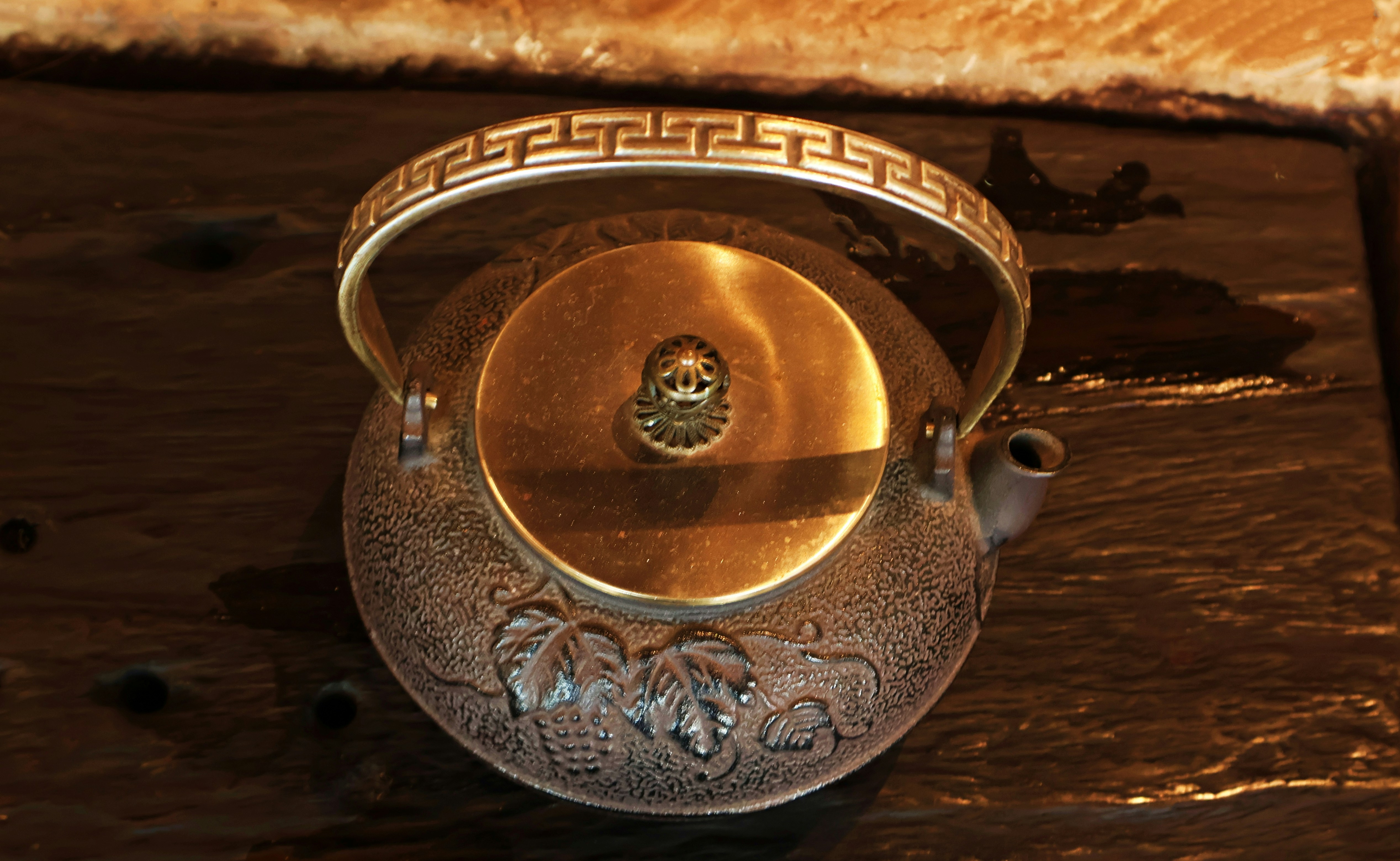 An old traditional Tea Kettle with very intricate design. | A decorative cast iron teapot with a golden lid.