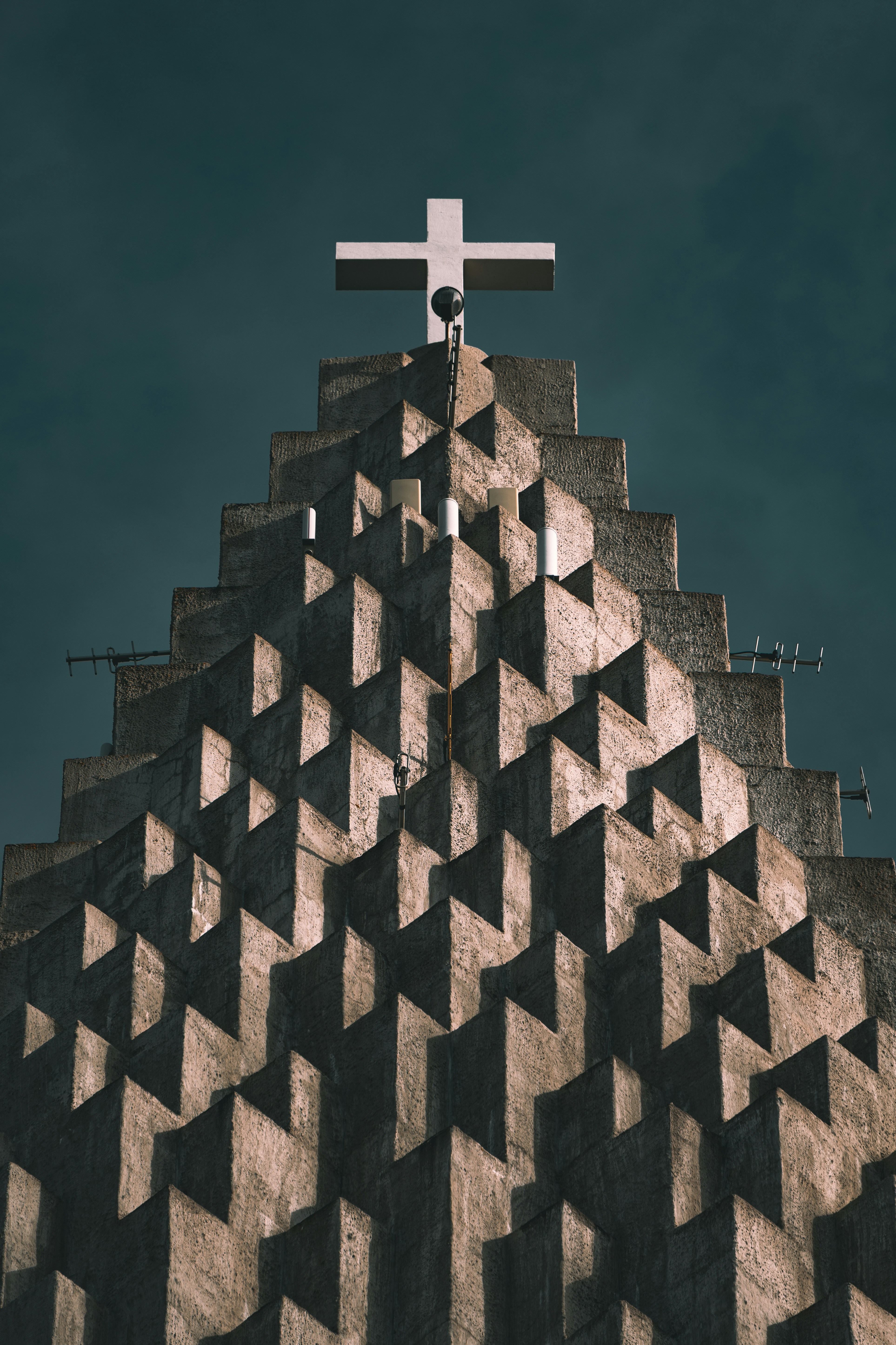 Geometric concrete church steeple with a white cross.