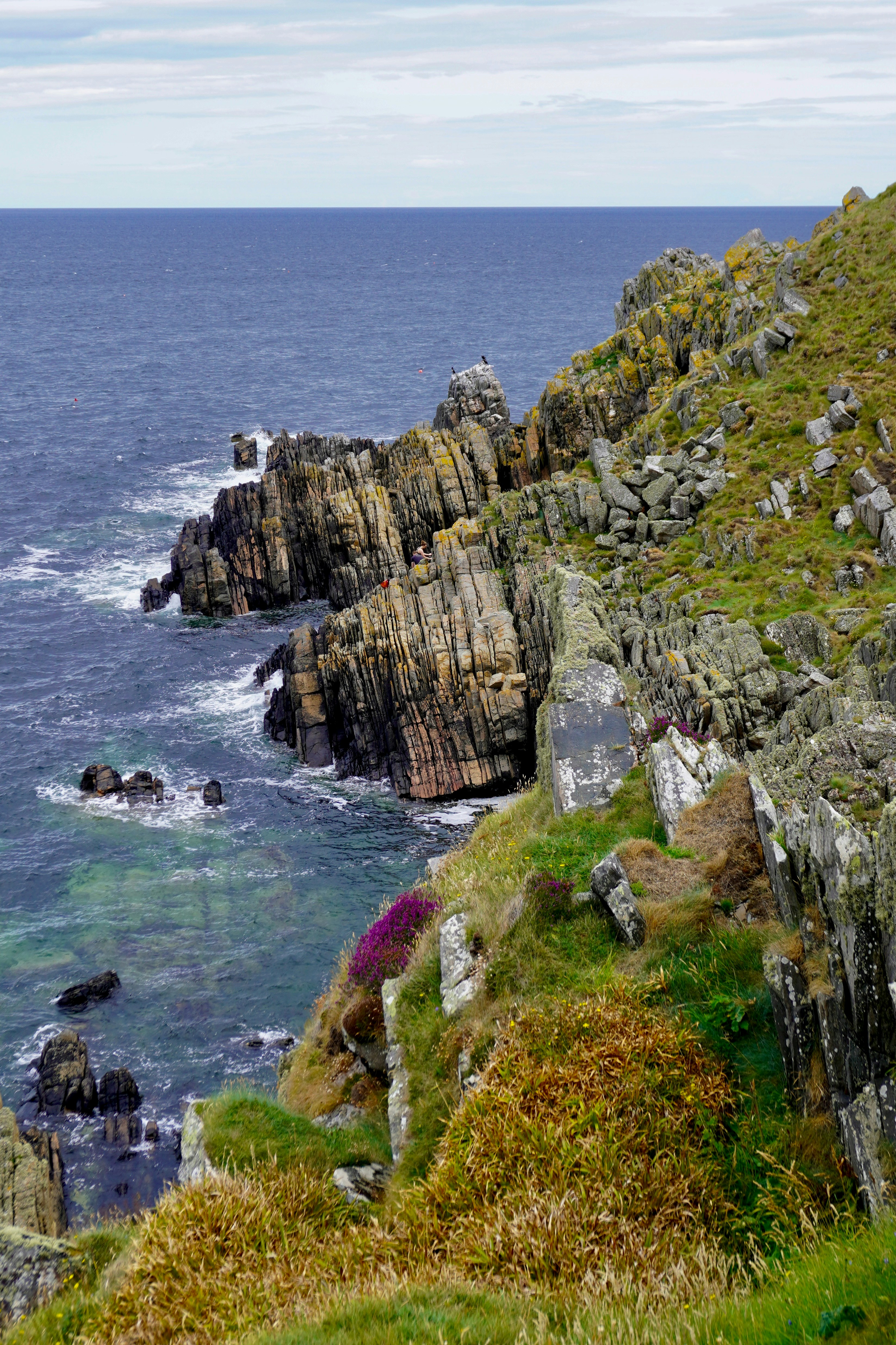 Rocky coastline with crashing waves under a cloudy sky.